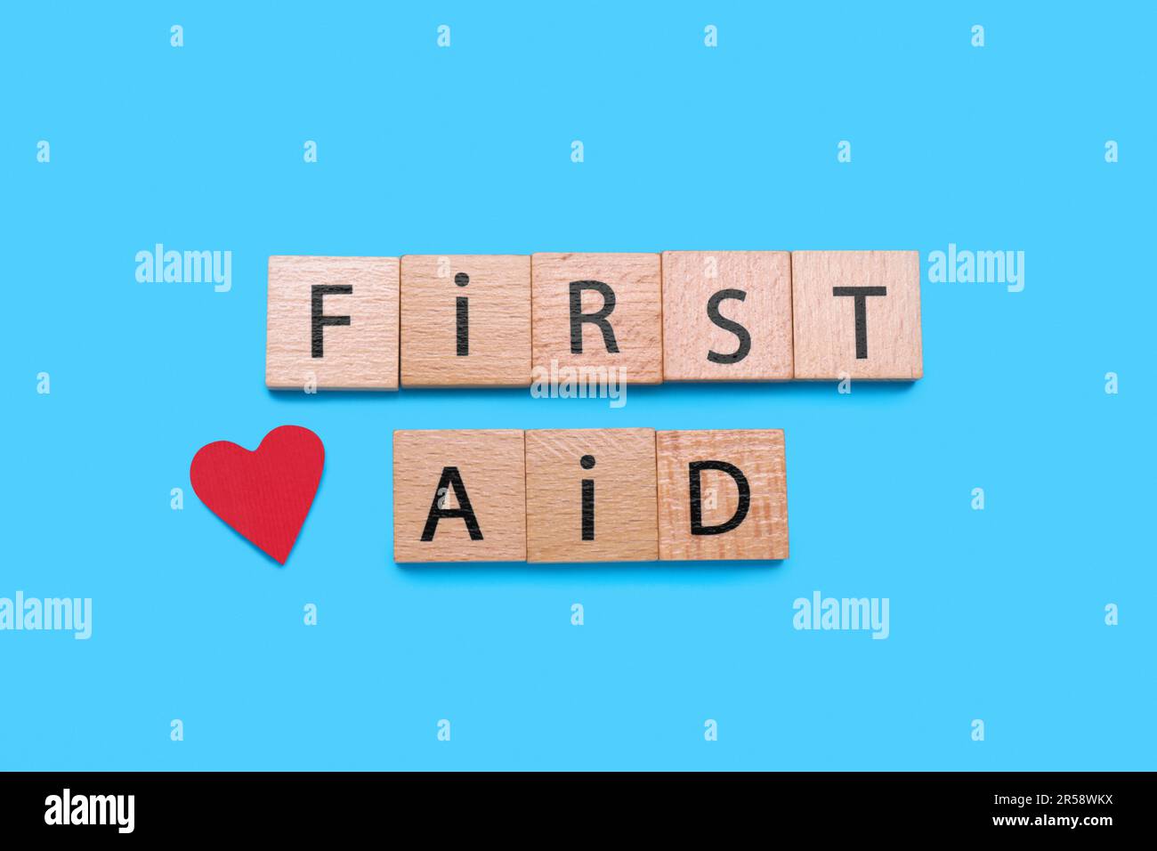 Words First Aid made of wooden cubes and cardboard heart on light blue ...