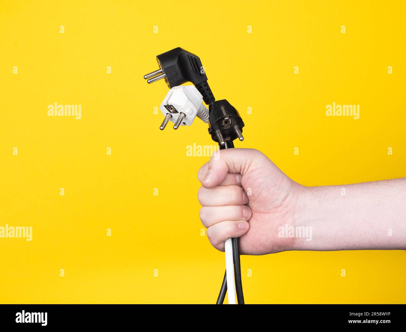 A male hand holds three electric plugs. No face, yellow background ...