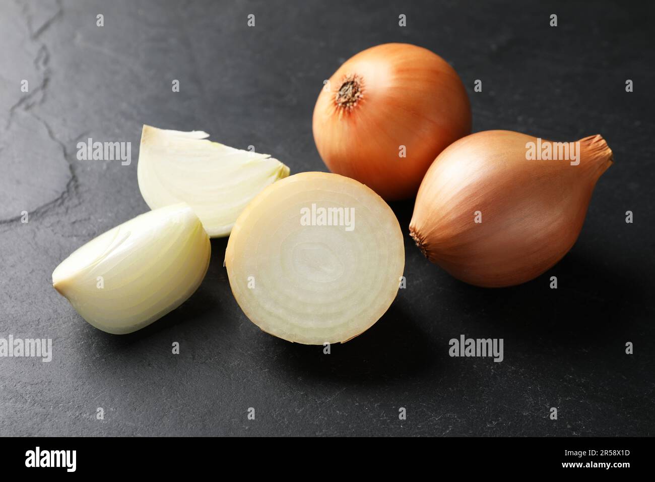 Whole and cut onions on black textured table Stock Photo - Alamy
