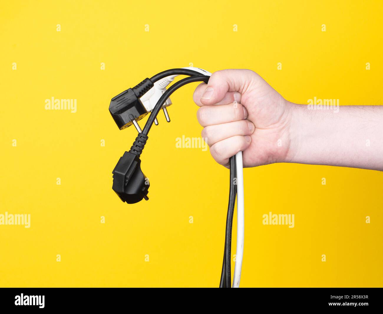 A male hand holds three electric plugs. No face, yellow background ...