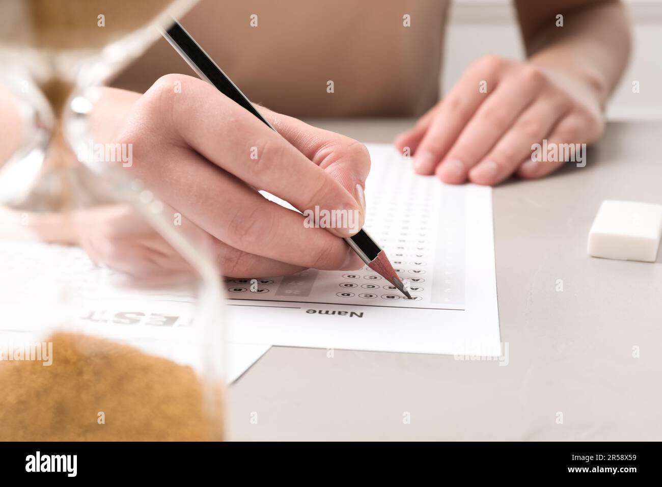 Student filling answer sheet at light grey table, closeup. Passing exam ...