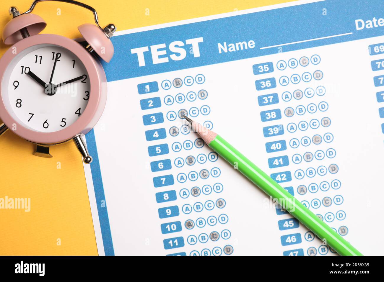 Answer sheet, pencil and alarm clock on yellow background, flat lay ...