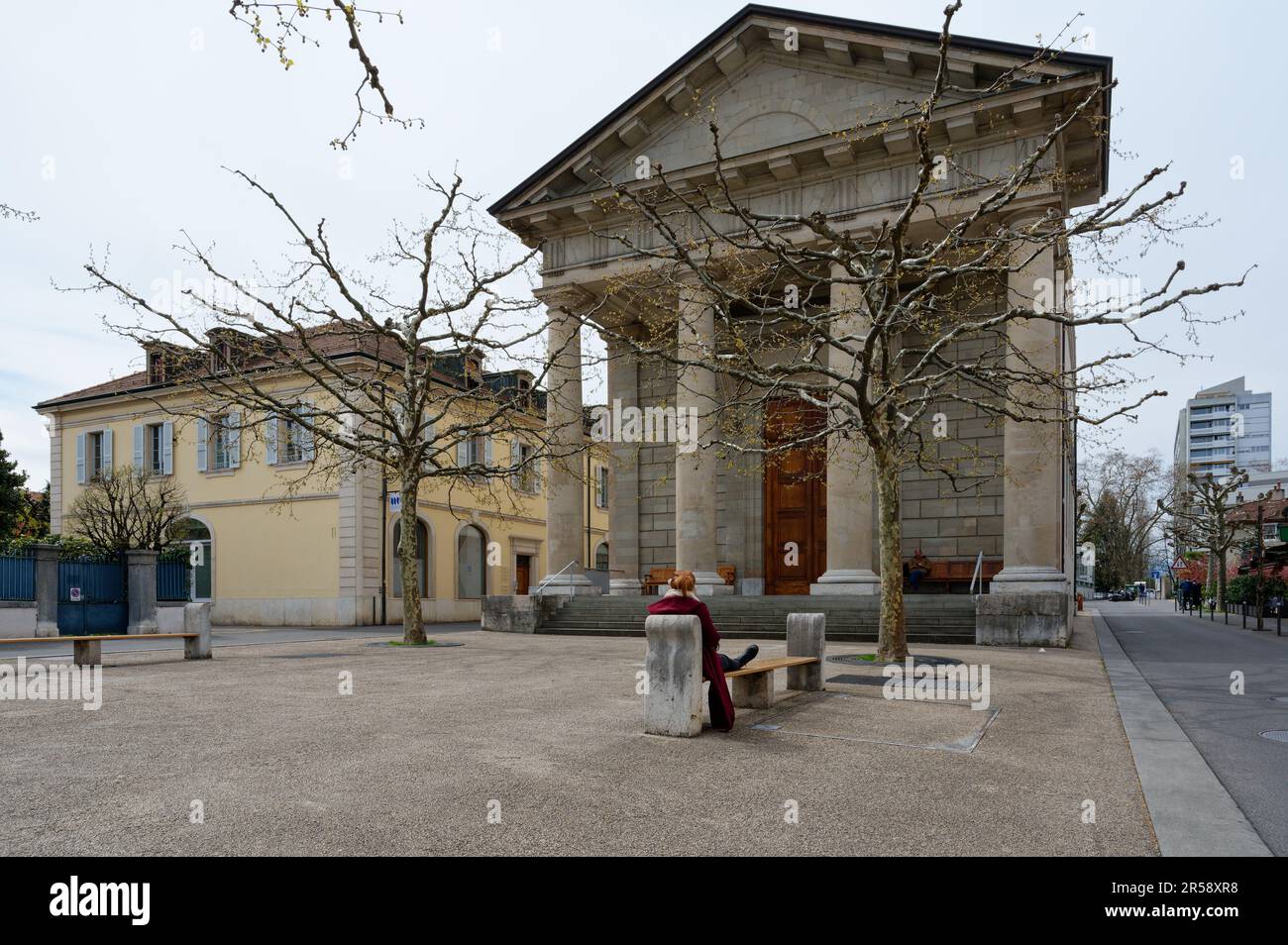 Red headed woman with a red coat sitting comfortably in a bench outside ...