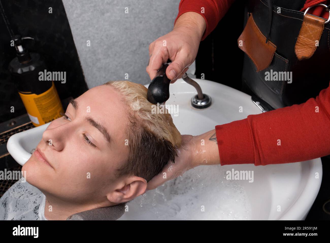 Barber washes his head and hair with rain in the sink to a young ...