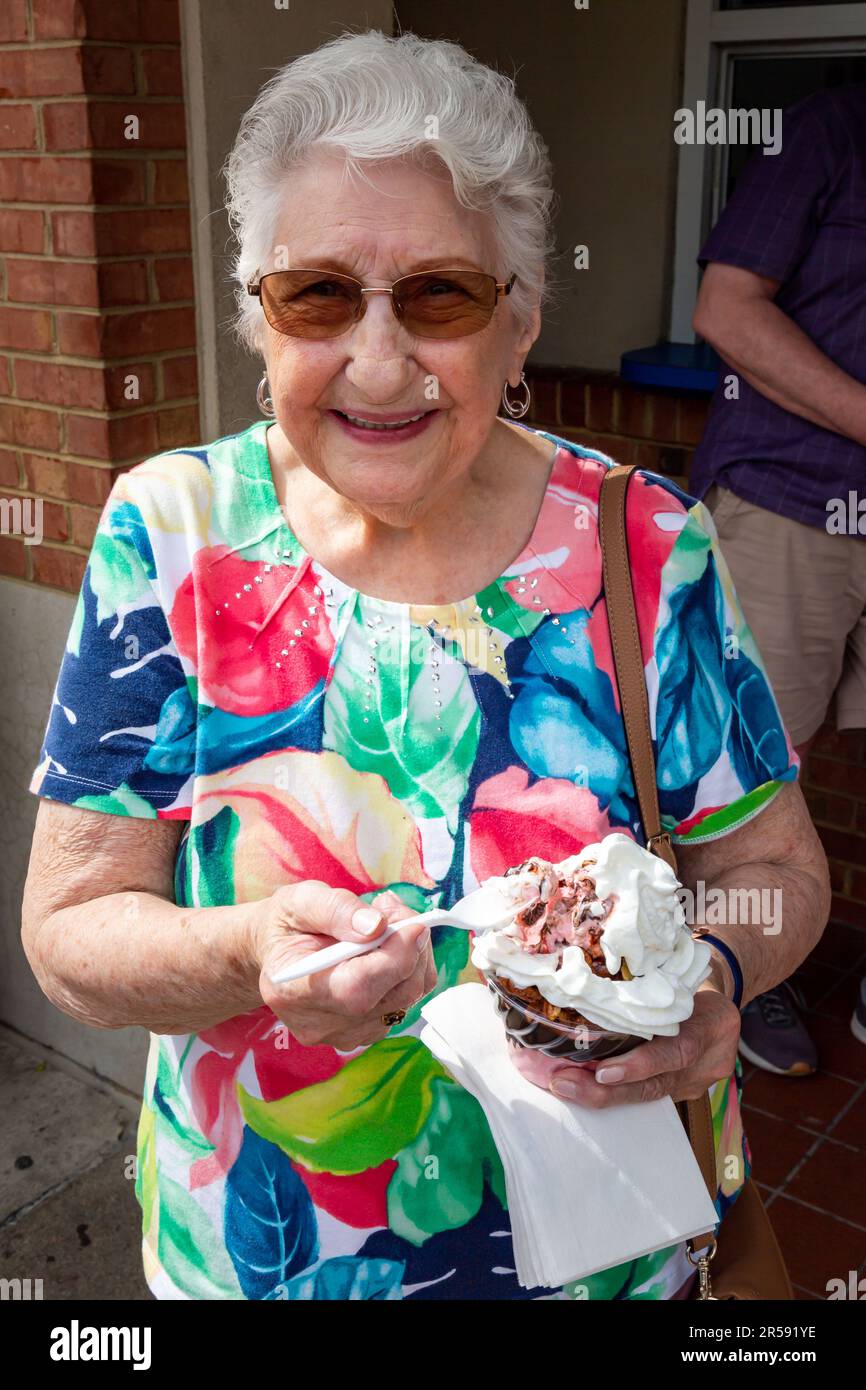 An elderly woman in a colorful shirt smiles as she's about to eat an ...