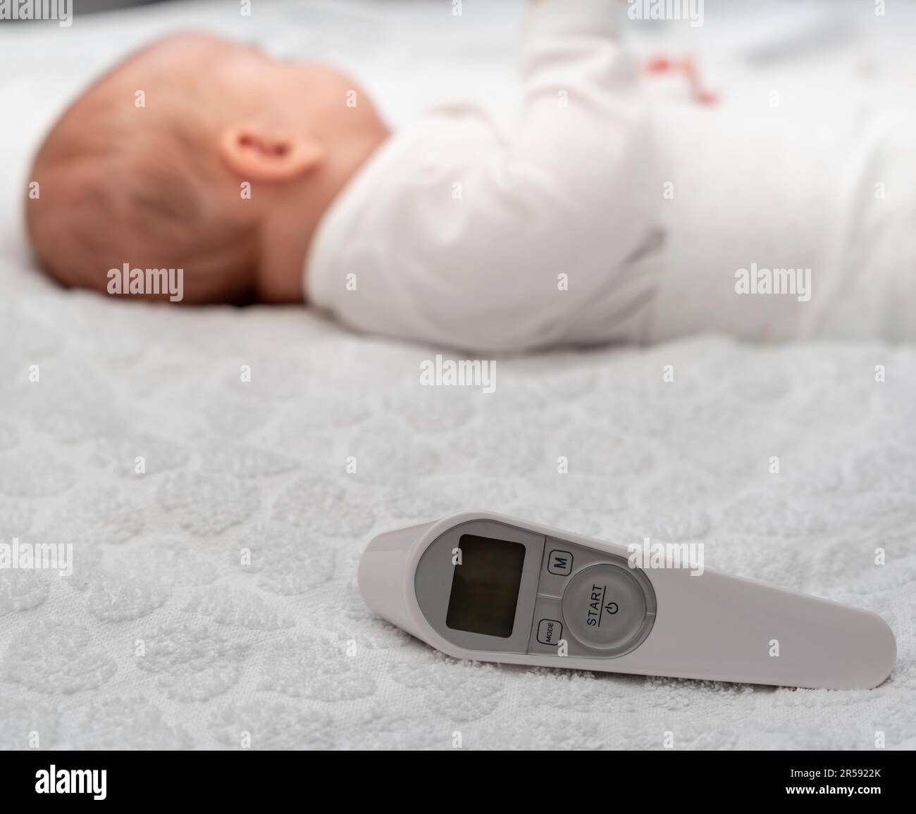 Infrared thermometer and a newborn baby in the background as a concept ...