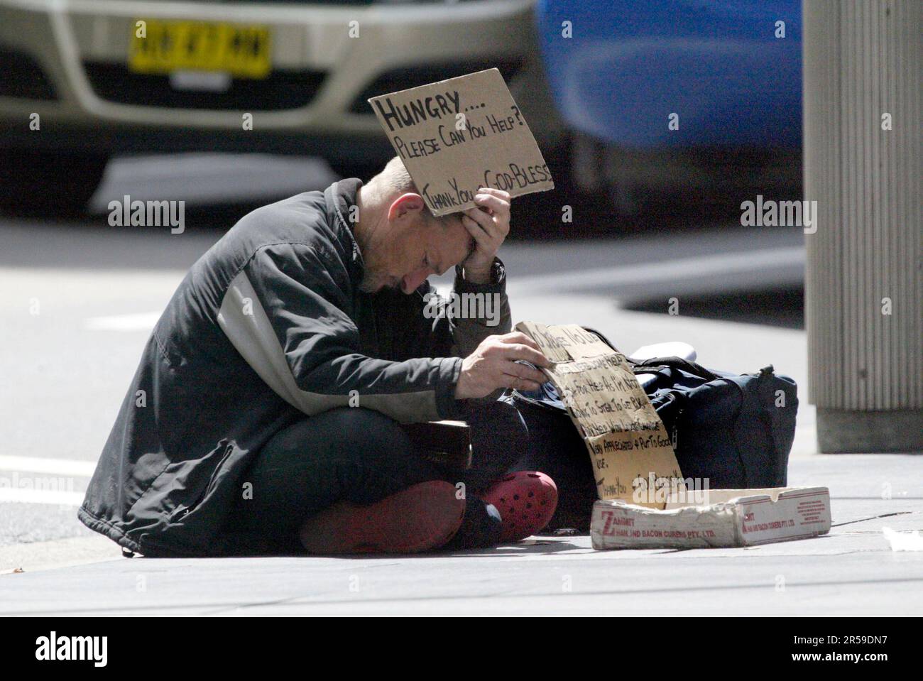 A homeless man begs with the aid of a placard on George Street at ...