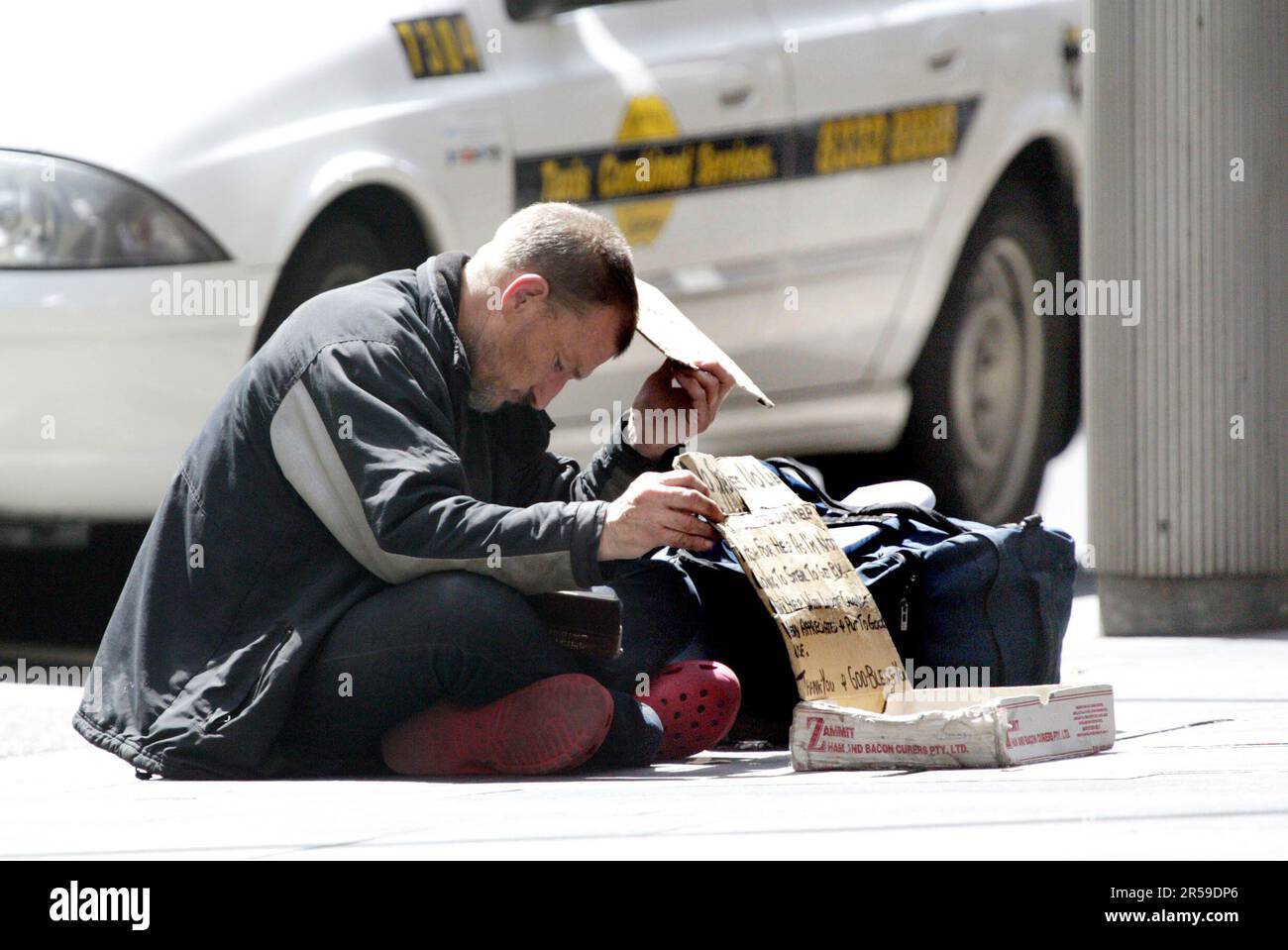 A homeless man begs with the aid of a placard on George Street at ...
