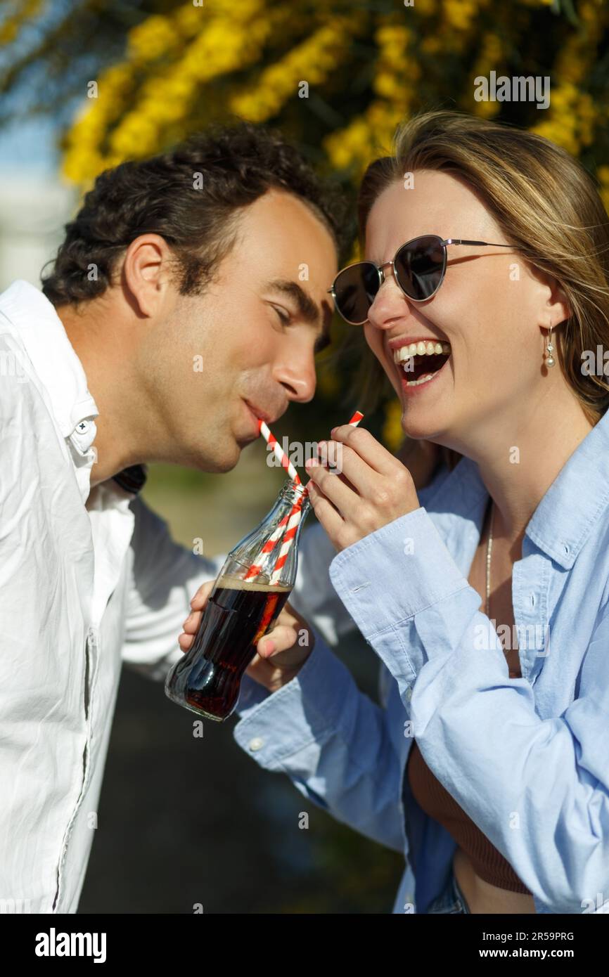 Young Happy Couple Outdoors Drinking Cold Drink From Glass Bottle With Straw Side View Of Man