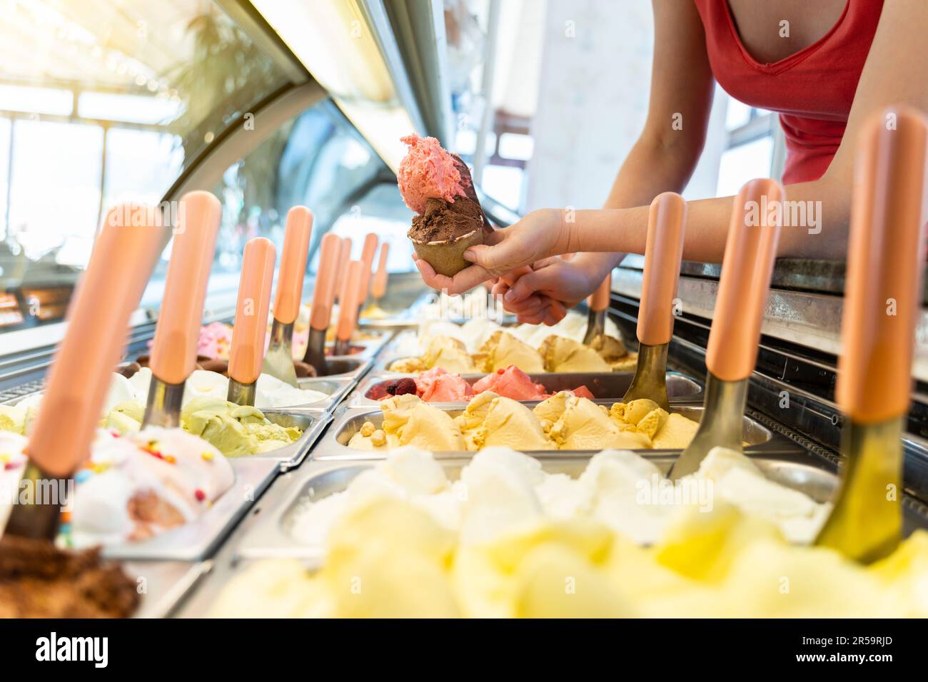 Ice cream showcase with a saleswoman preparing a tub with two flavors ...