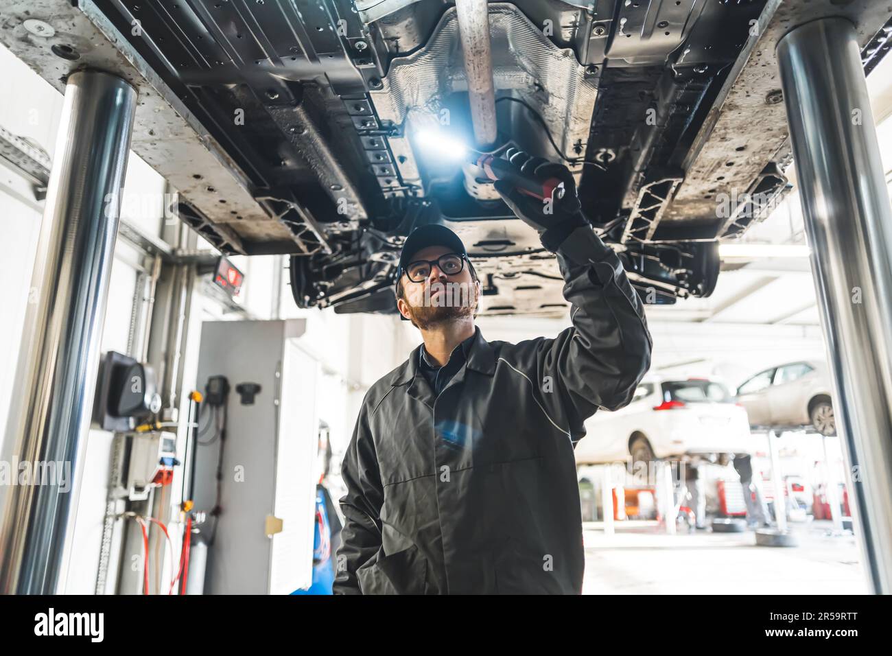 Auto mechanic with LED work light inspecting car chassis standing under ...