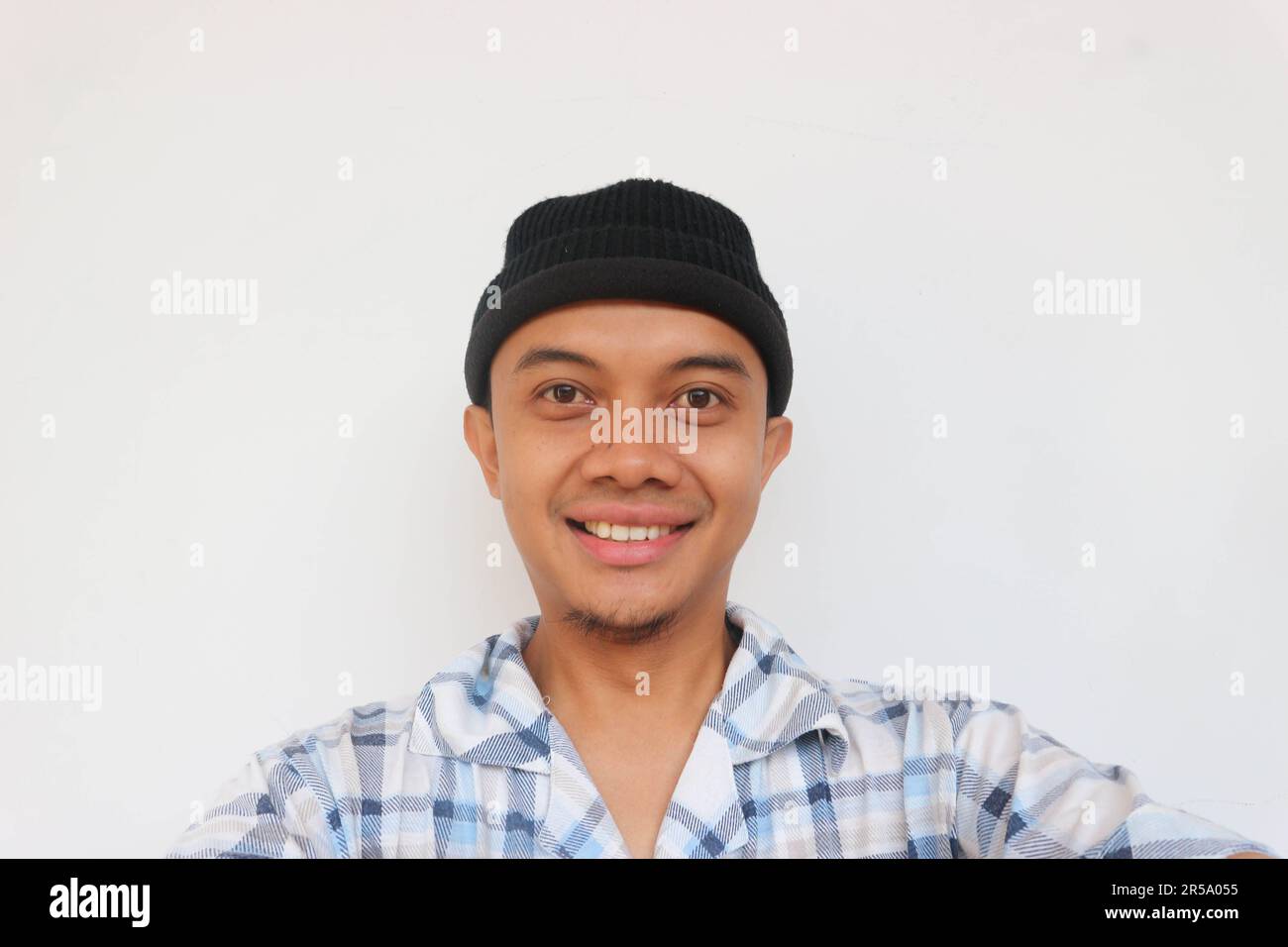 Man wearing pajamas and beanie cap smiling while looking at camera ...