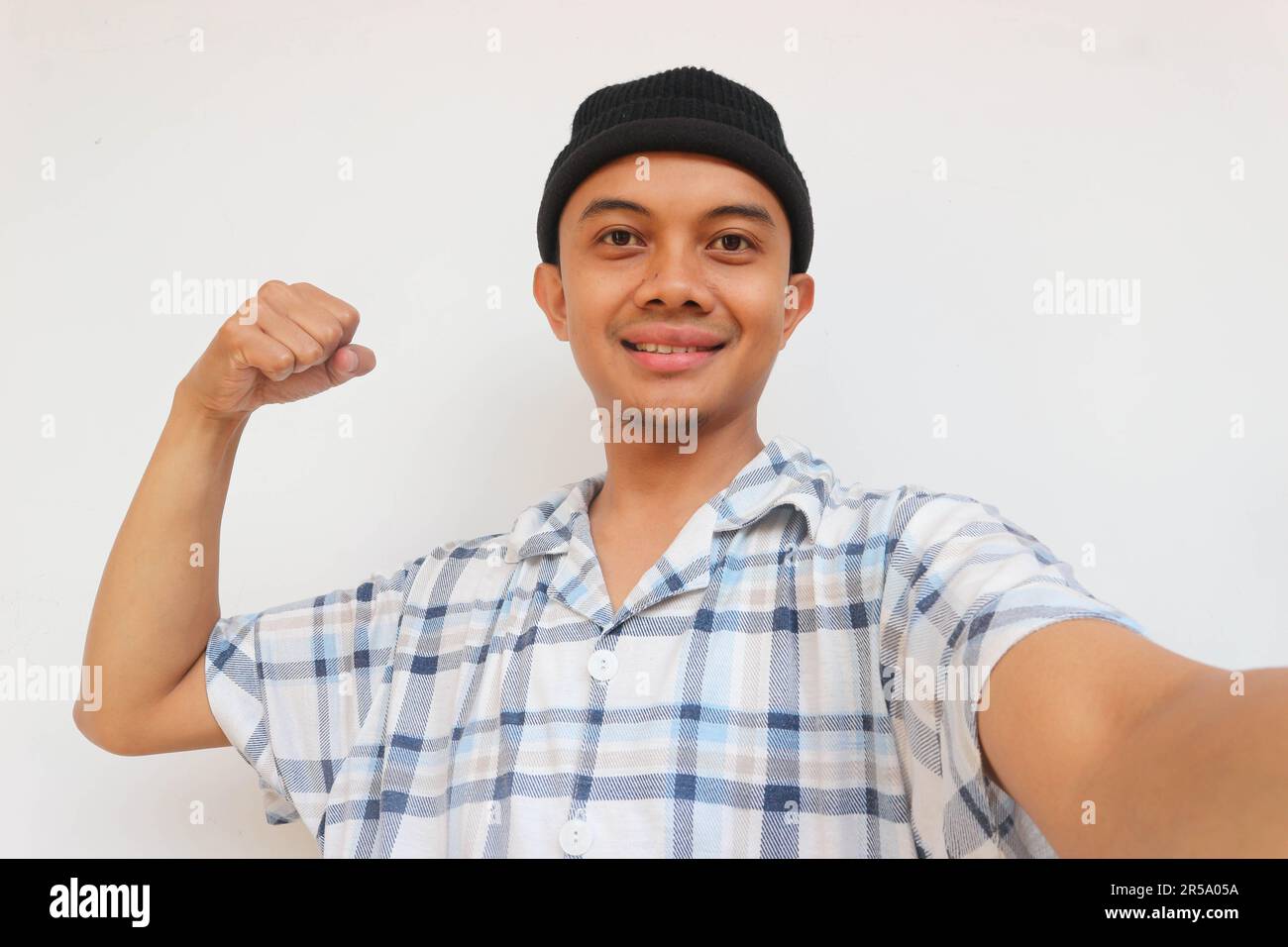 Smiling adult man wearing pajamas and beanie cap showing his bicep ...