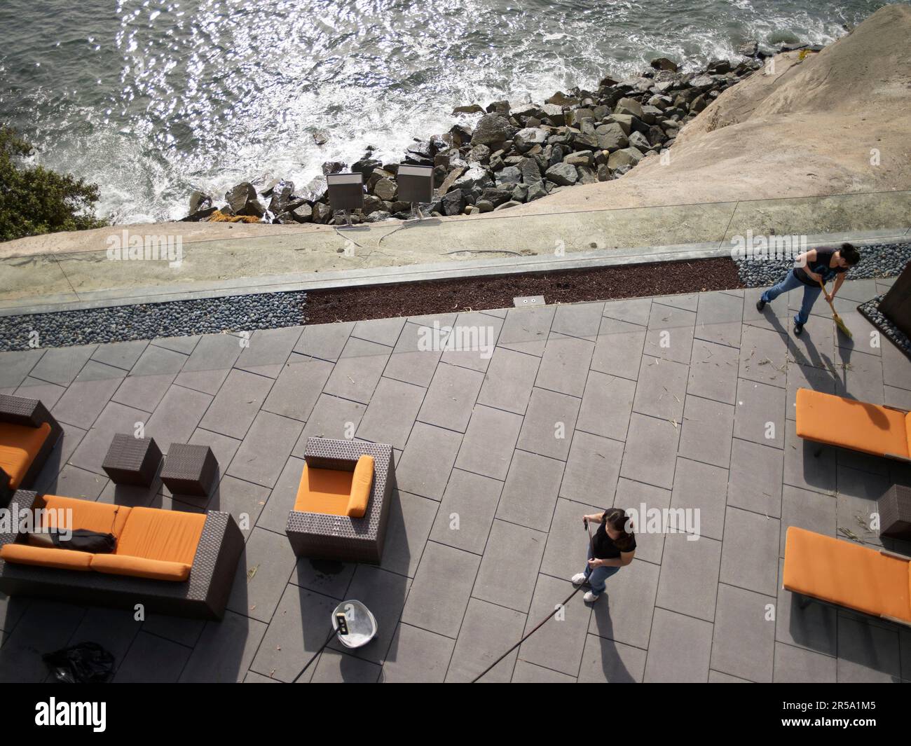 Two cleaning ladies sweep and clean the patio of an oceanfront home in ...