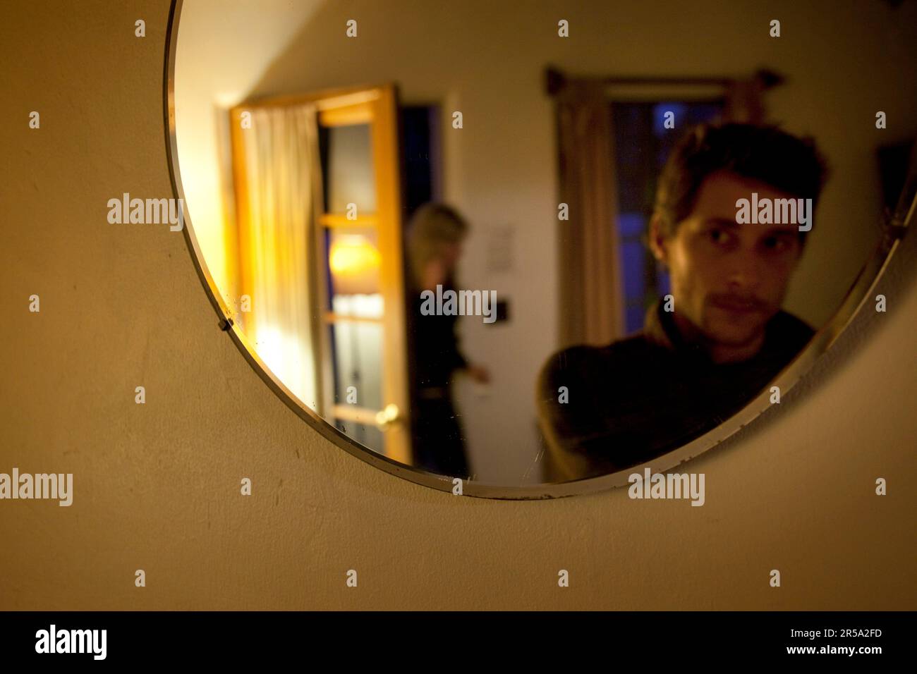 A man looks back through a mirror as a woman enters the room ...