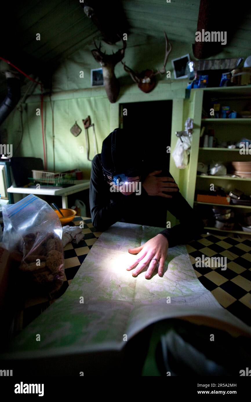 One man wearing a headlamp and looking at a map in a rustic cabin with ...