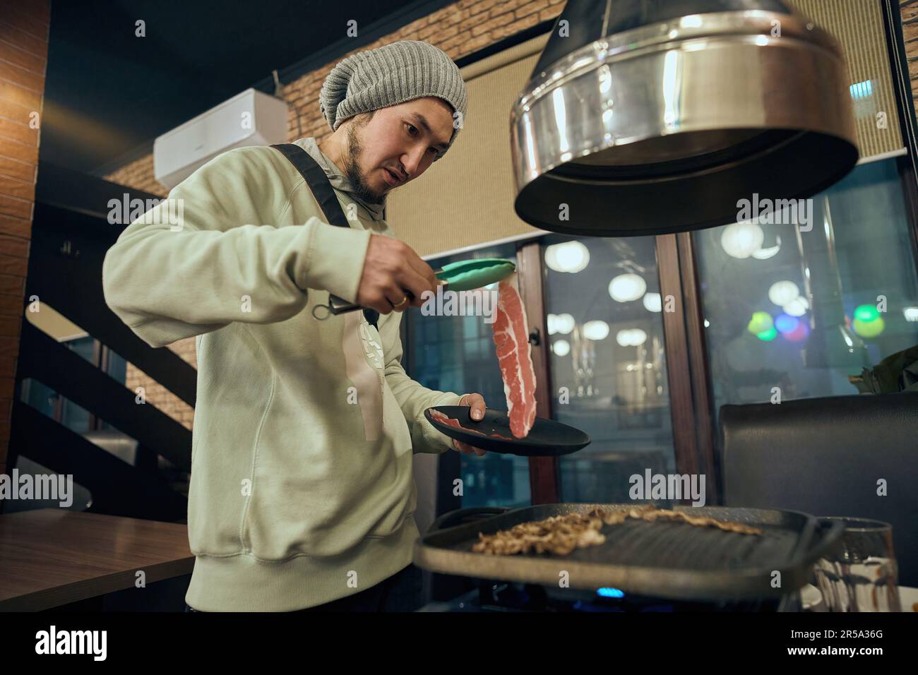 Asian woman cooks meat into the skillet on the stove in the reas Stock ...