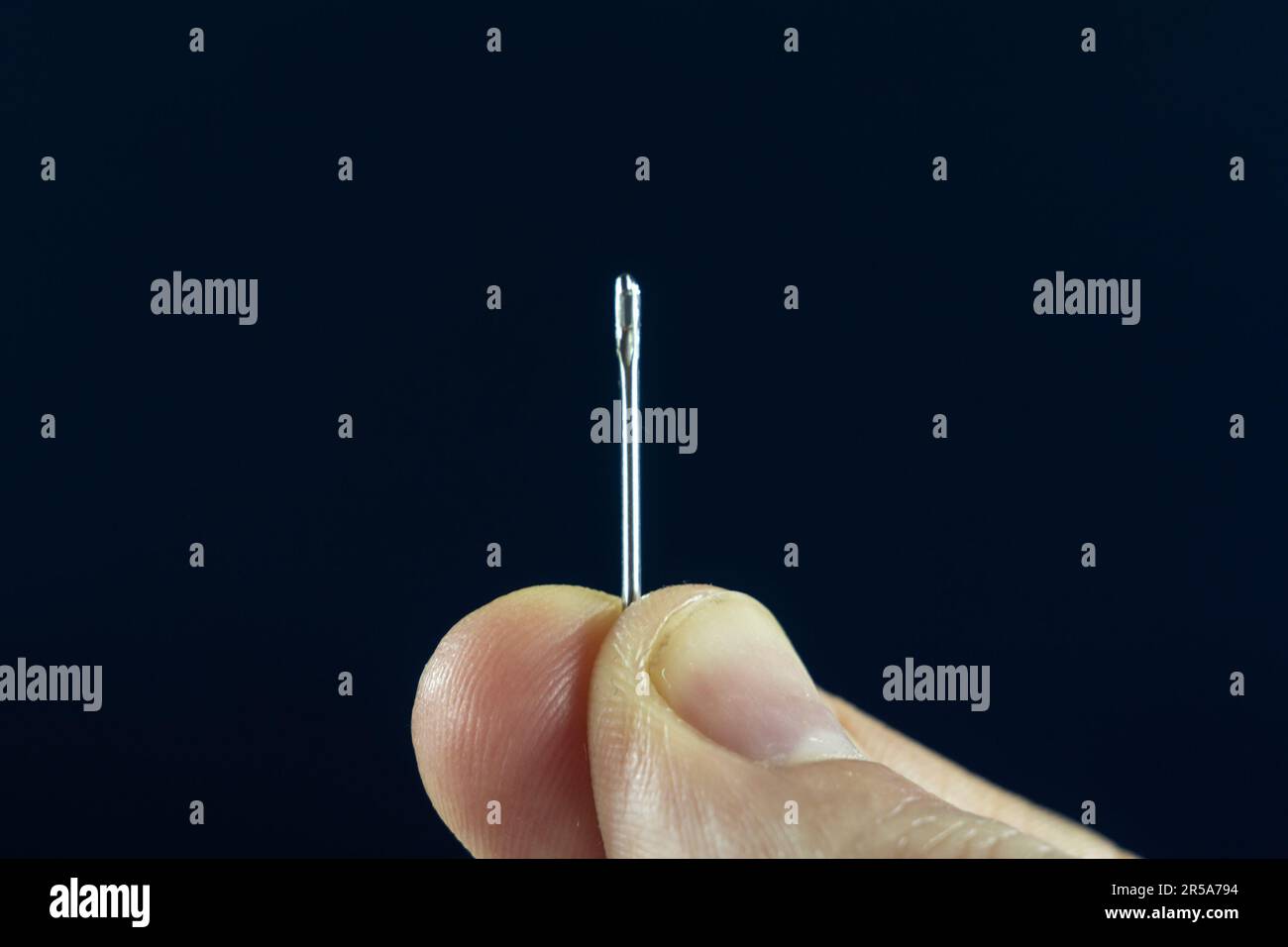 Picture of a sewing needle of metal held by fingers, isolated on a ...