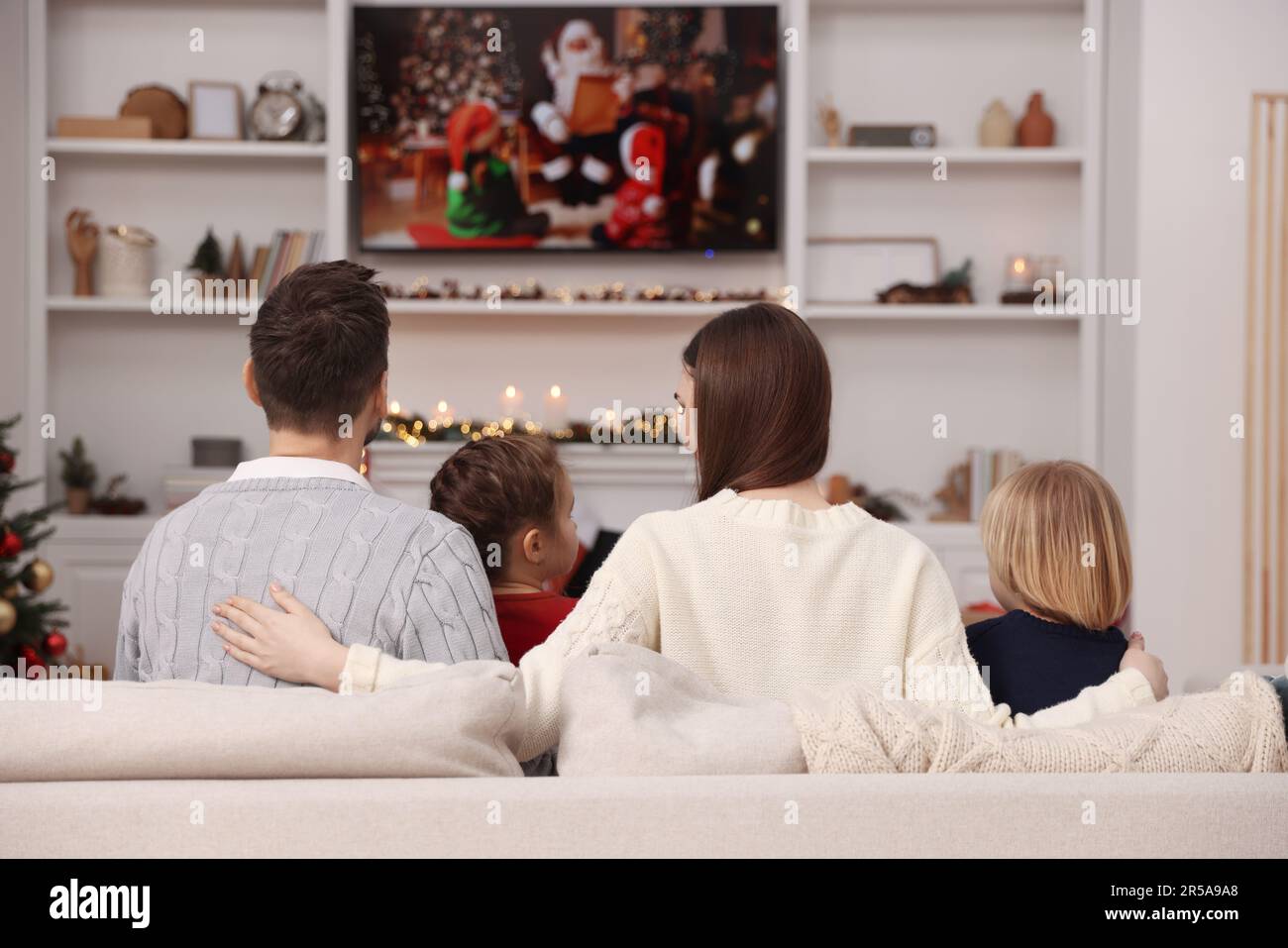 Family watching Christmas movie via TV in cosy room, back view. Winter ...
