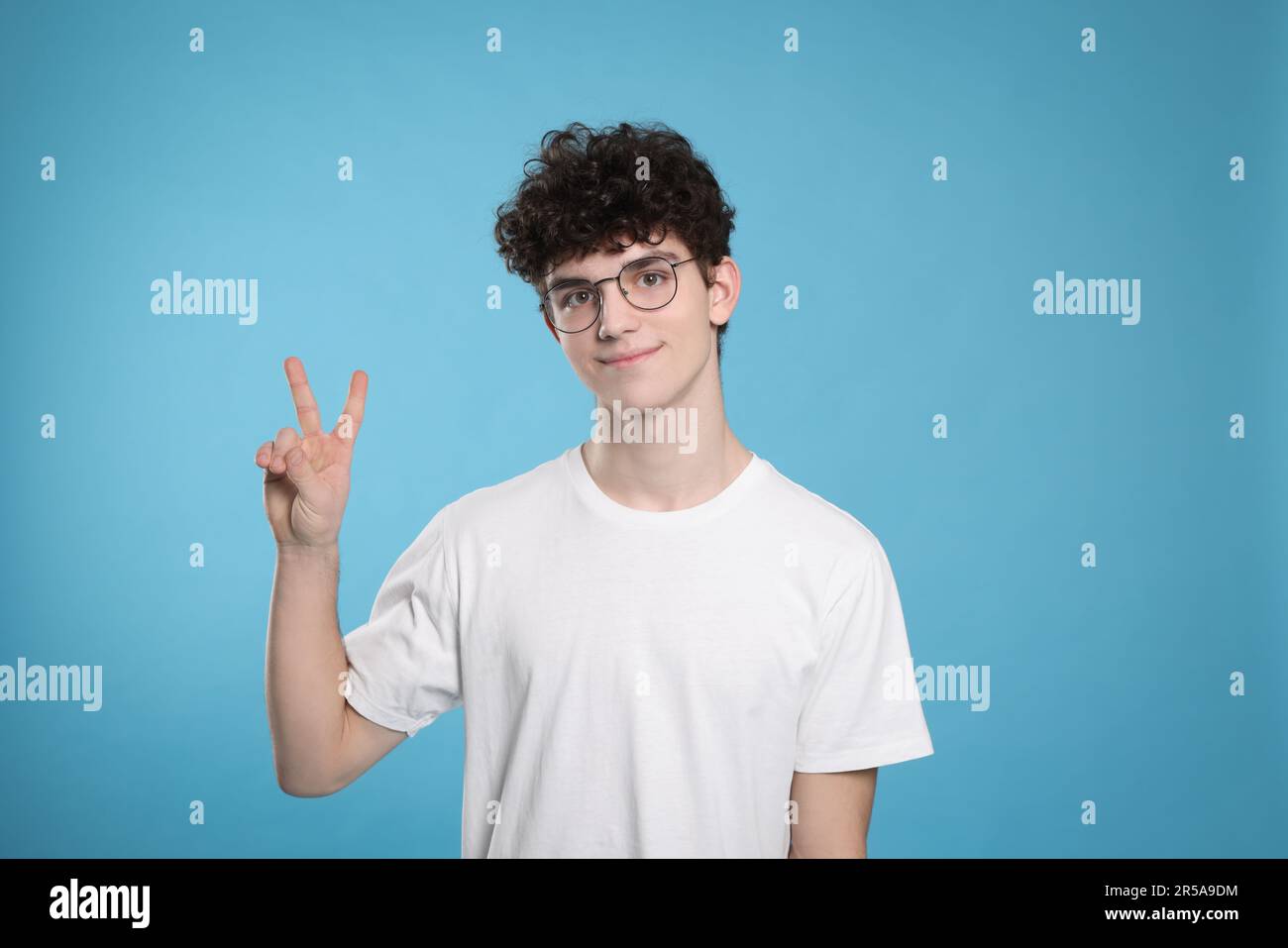 Portrait of cute teenage boy wearing glasses and showing peace gesture ...
