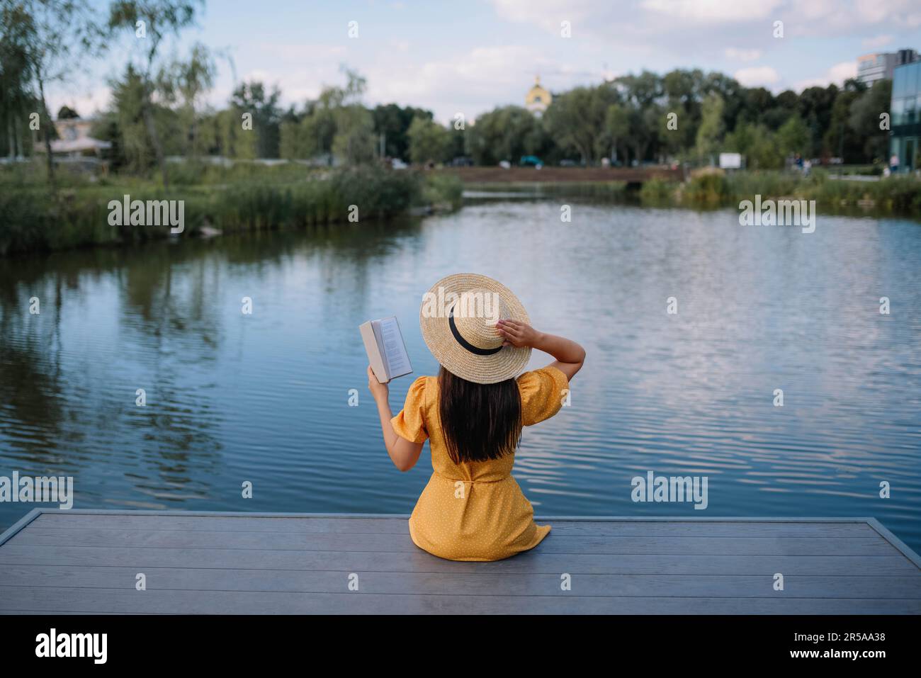 Woman reading book on pier near lake, back view Stock Photo - Alamy