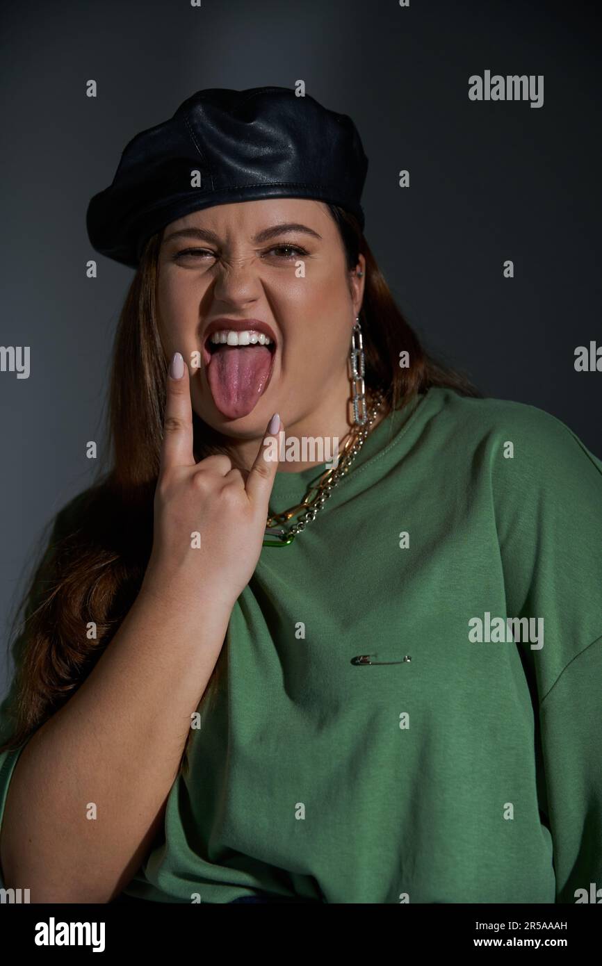 portrait of stylish plus size woman posing in leather beret and green t ...