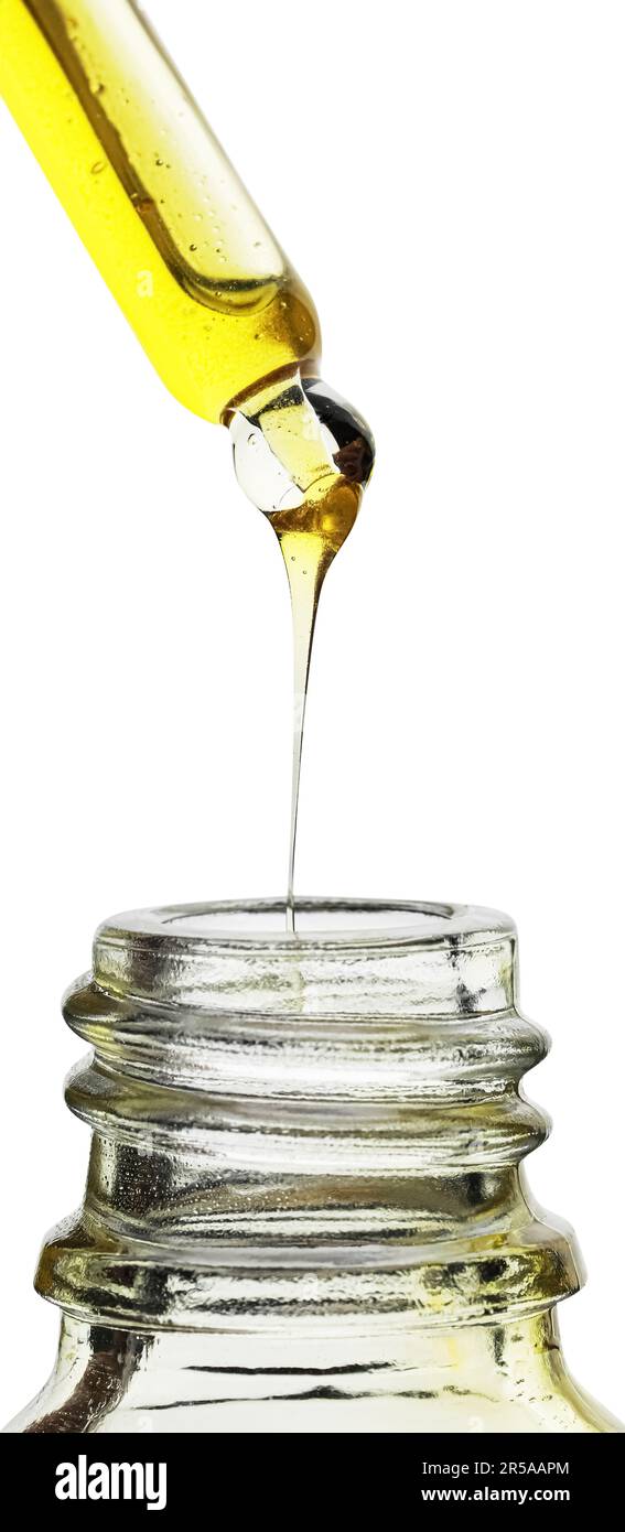 Dripping yellow facial serum from pipette into glass bottle on white ...
