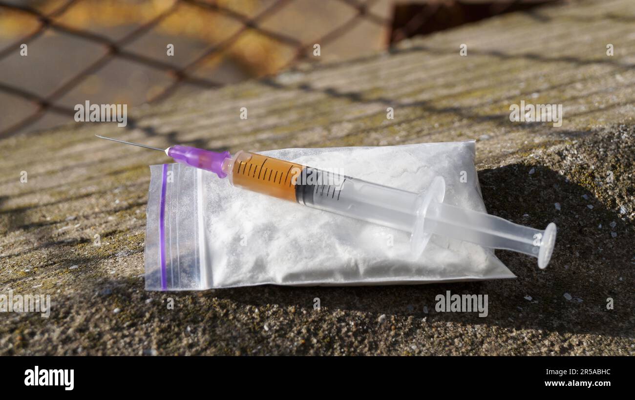 Plastic bag with powder and syringe on stone surface outdoors, closeup ...