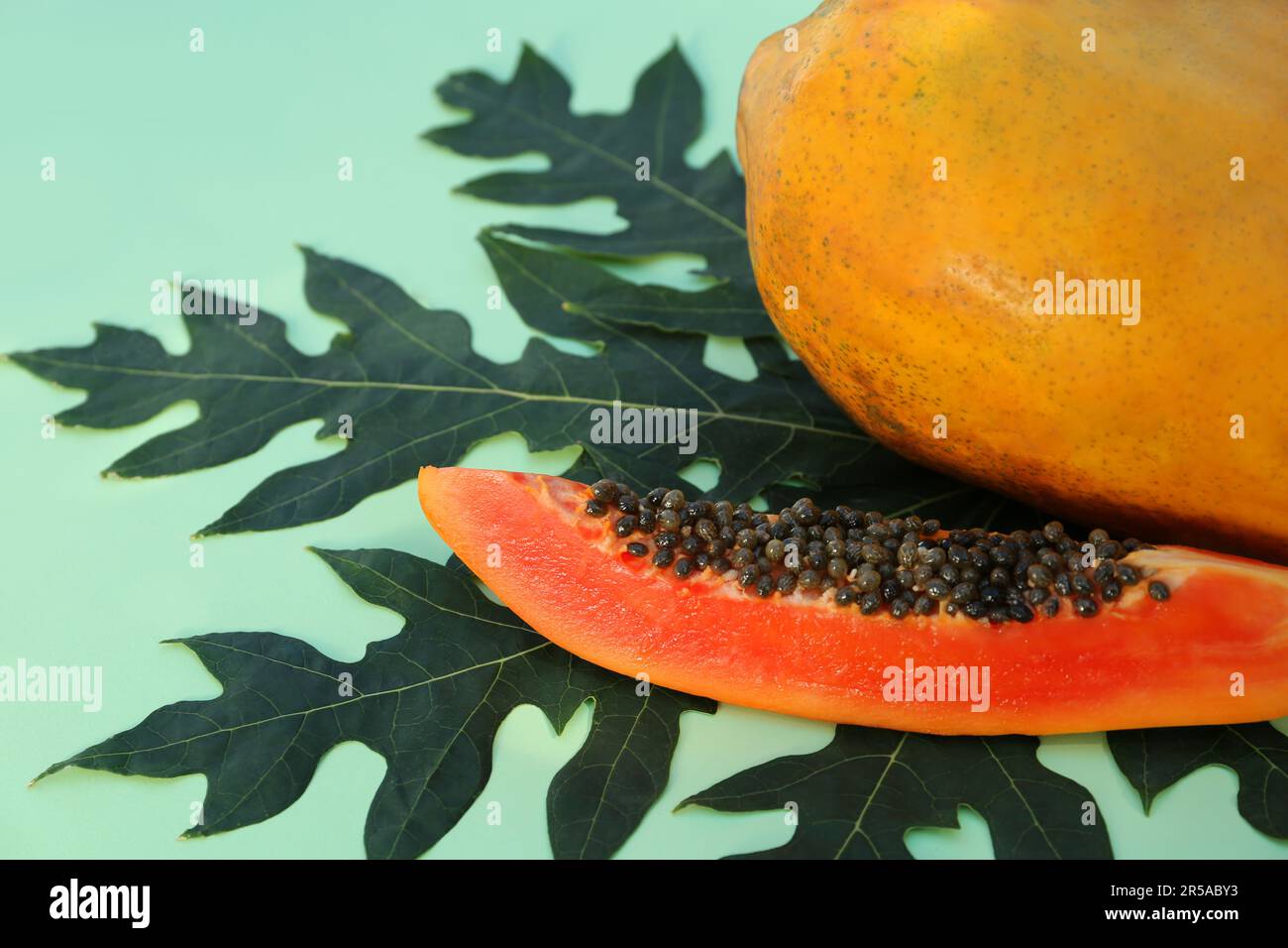 Whole and cut fresh ripe papaya fruits with leaf on light green ...
