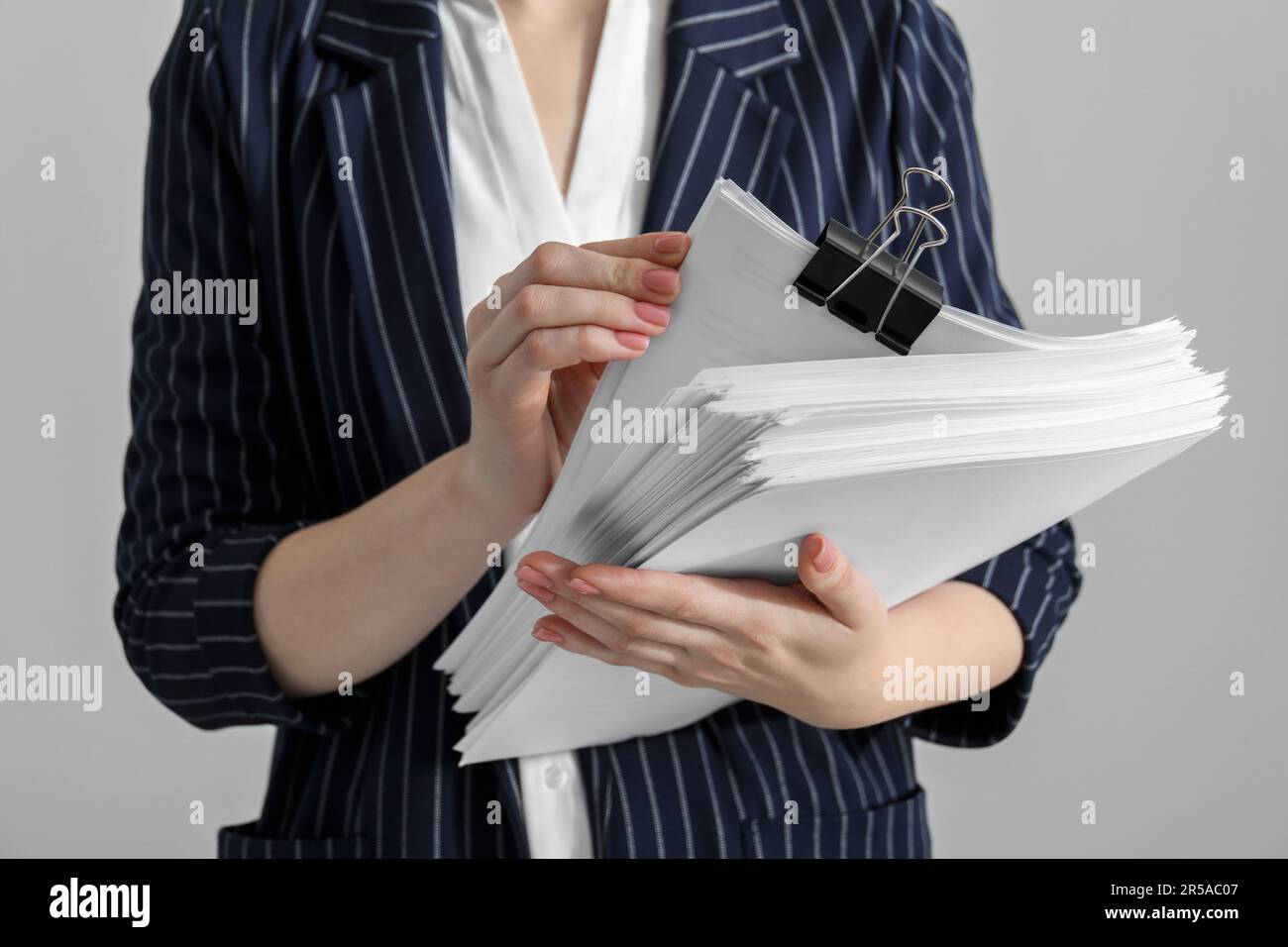 Woman attaching documents with metal binder clip on grey background ...