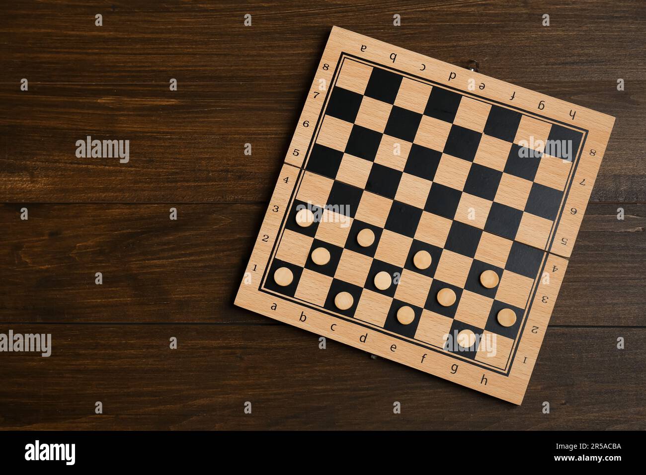 Checkerboard with game pieces on wooden table, top view. Space for text ...