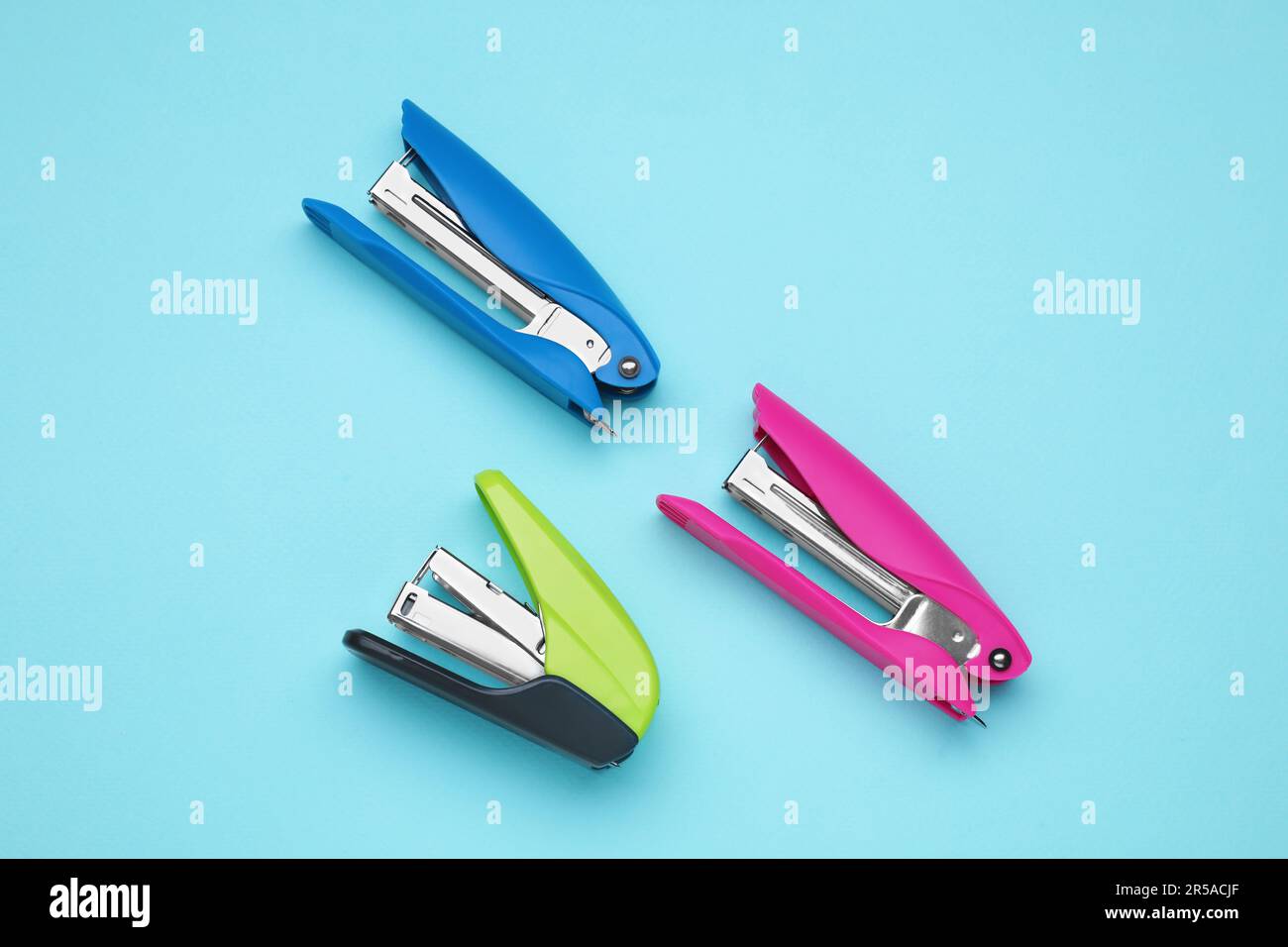 New bright staplers on light blue background, flat lay. School ...