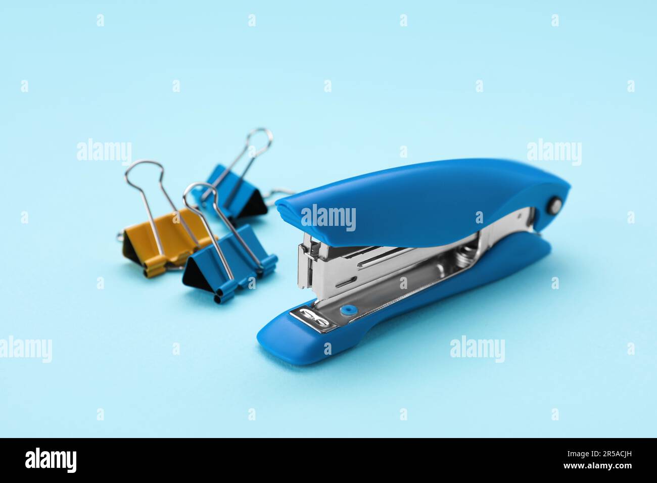 New bright stapler with binder clips on light blue background. School ...