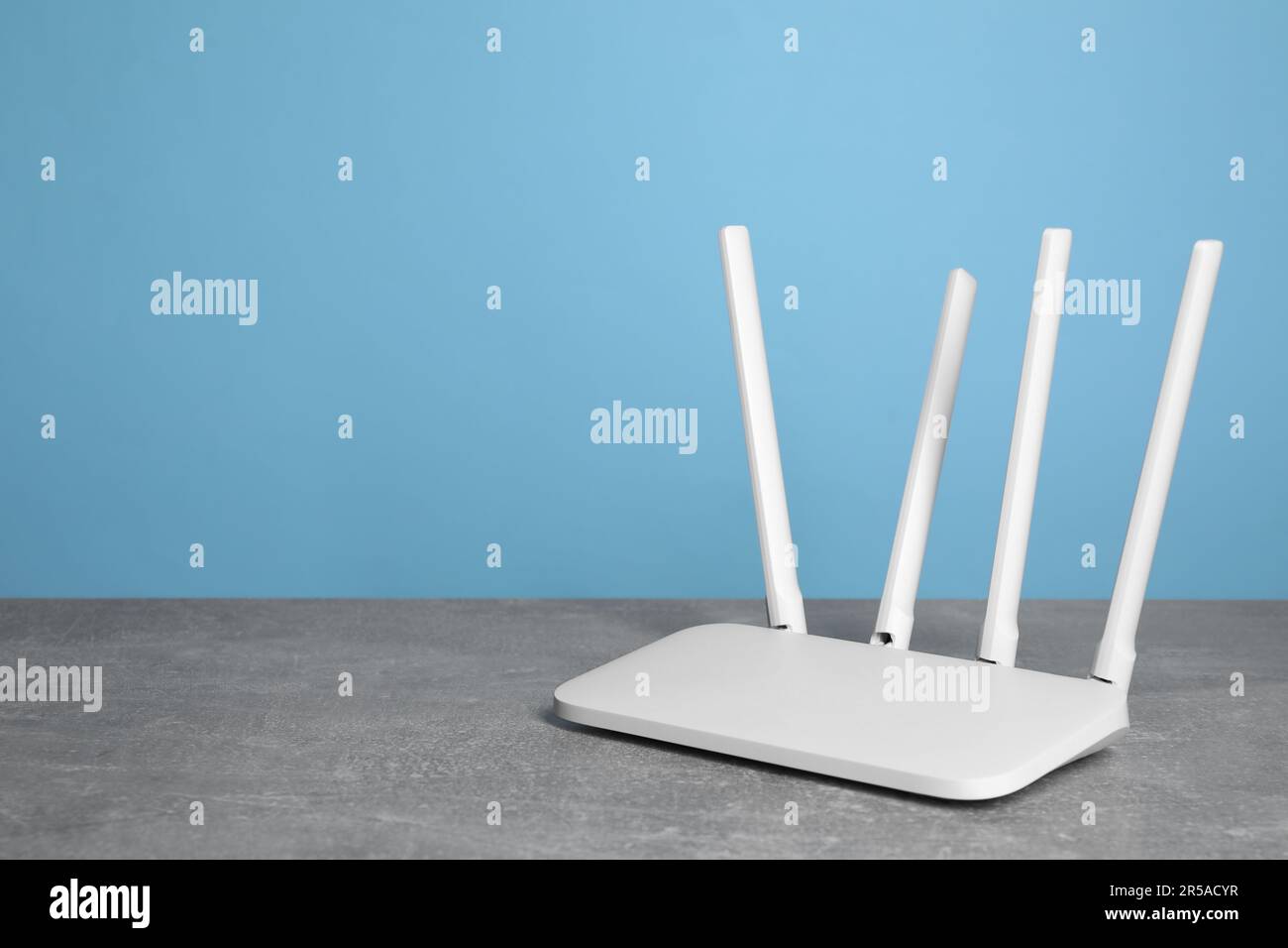 New white Wi-Fi router on grey textured table against light blue ...