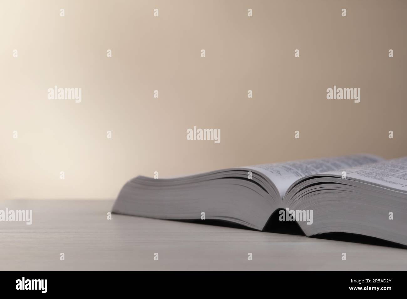 Open Bible on white wooden table against beige background. Space for ...