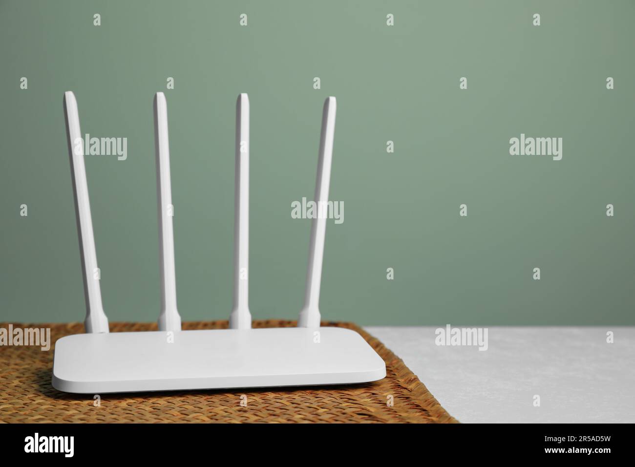 New modern Wi-Fi router on white table near green wall, space for text ...