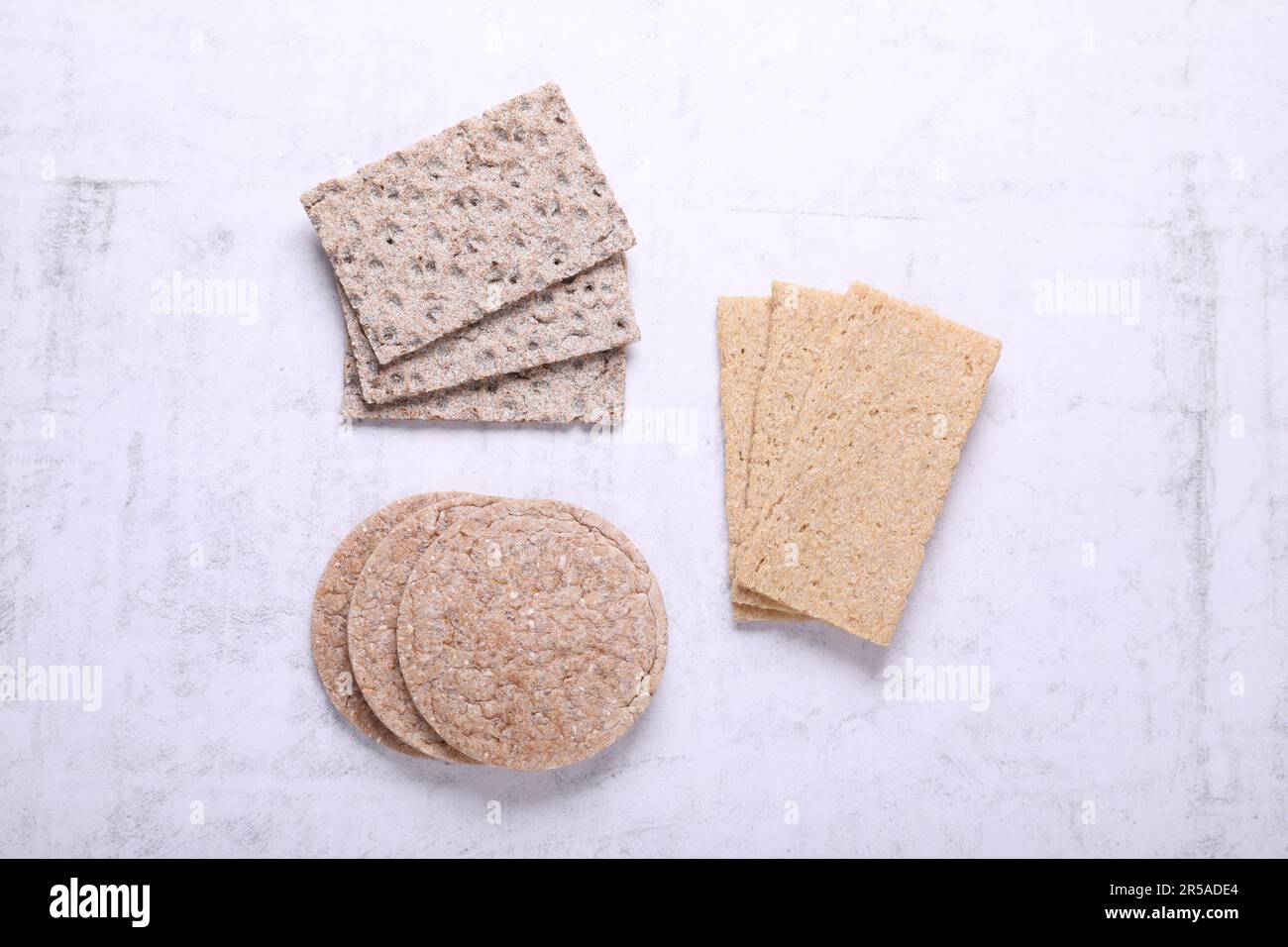Different types of tasty crispbreads on white textured table, flat lay ...