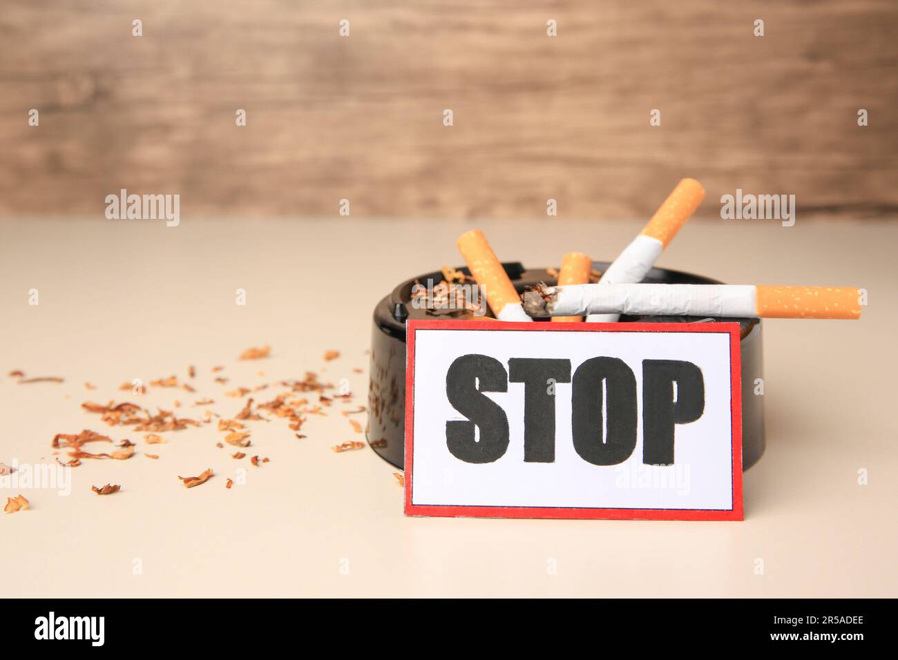 Card with word Stop, ashtray and cigarette stubs on beige background ...