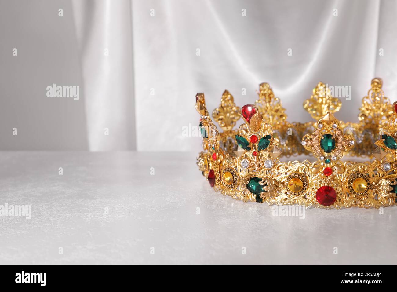 Beautiful golden crown with gems on light grey table. Space for text ...