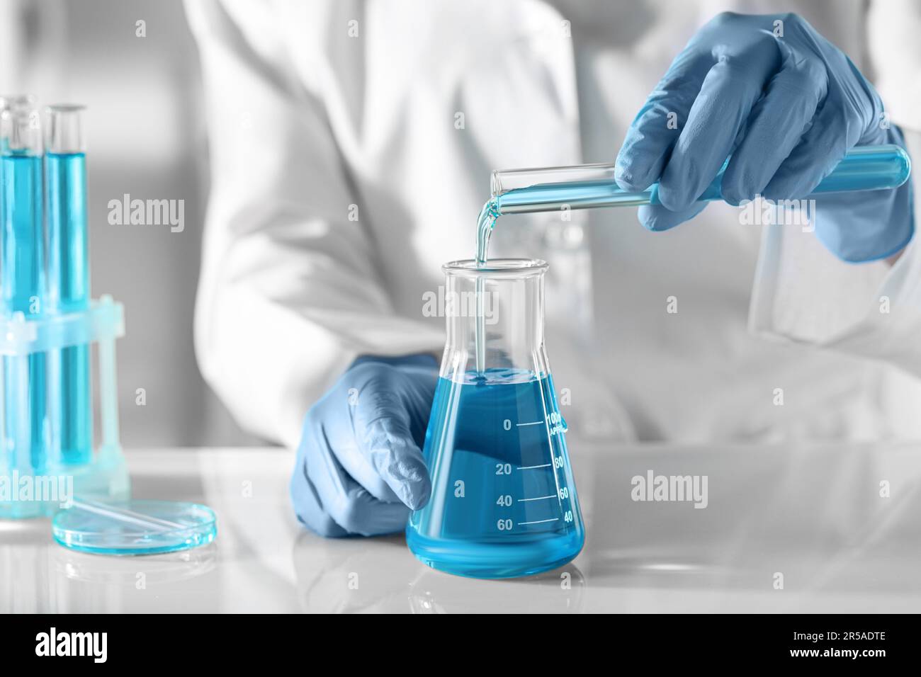 Scientist pouring light blue liquid from test tube into flask in ...