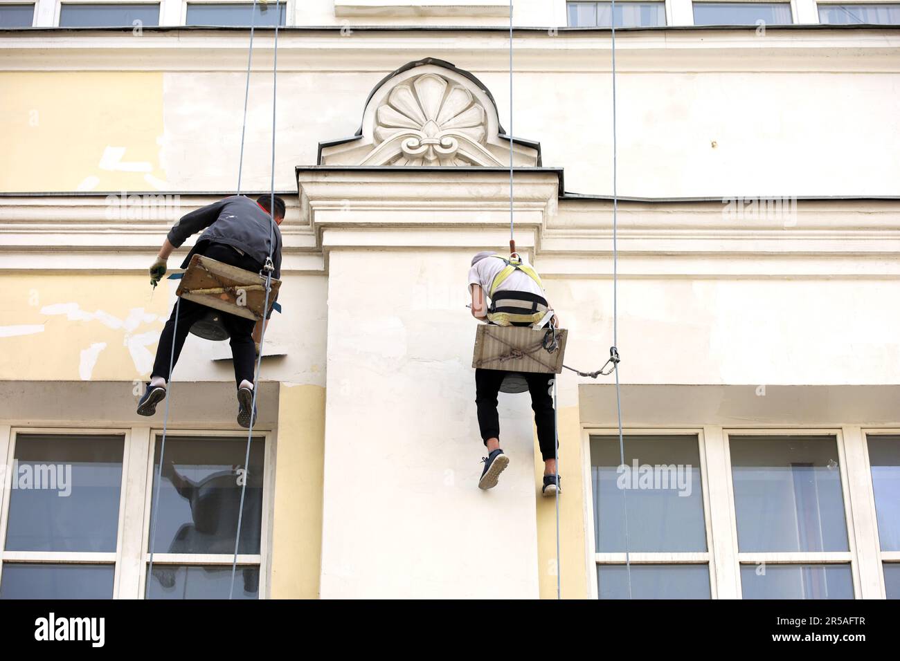 Workers paints the building wall. Painters hanging on a cable with ...