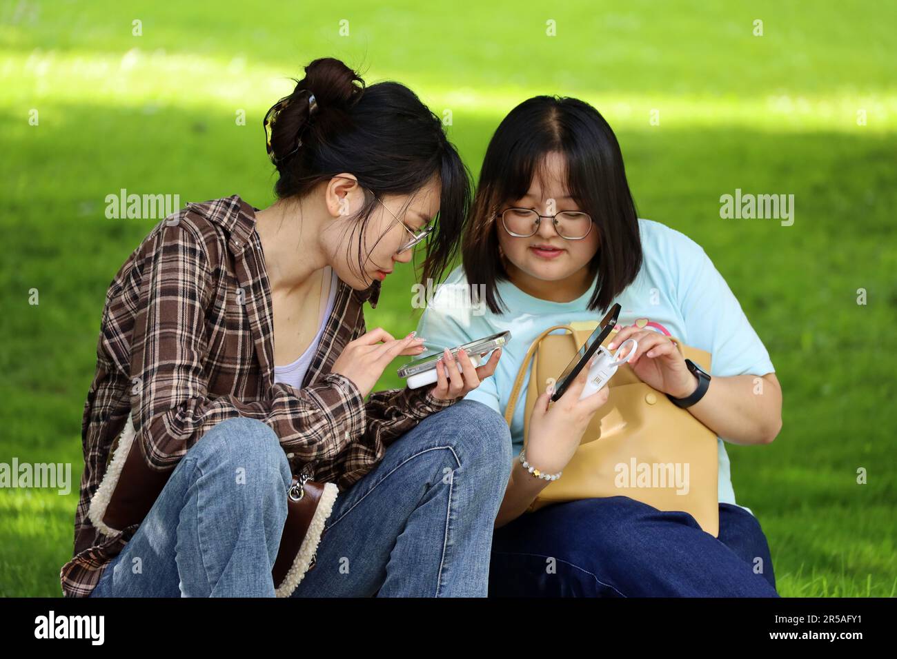 Two asian girls in eyeglasses look at smartphone screen sitting on city ...