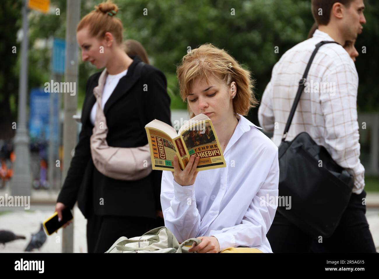 Girl sits on a street and reading book on walking people background ...