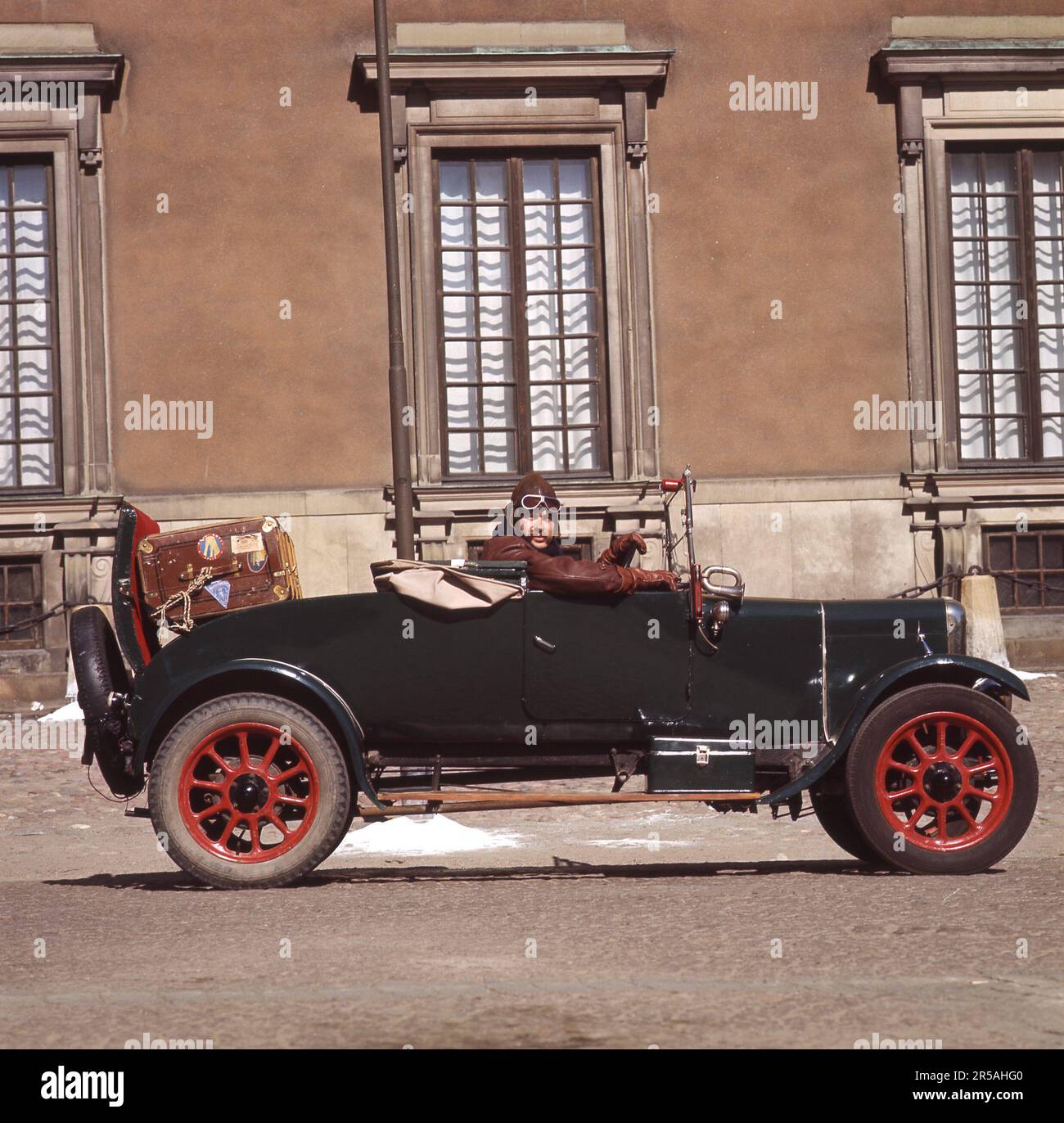 The old car. A man in a typical old fashioned driver's outfit complete ...