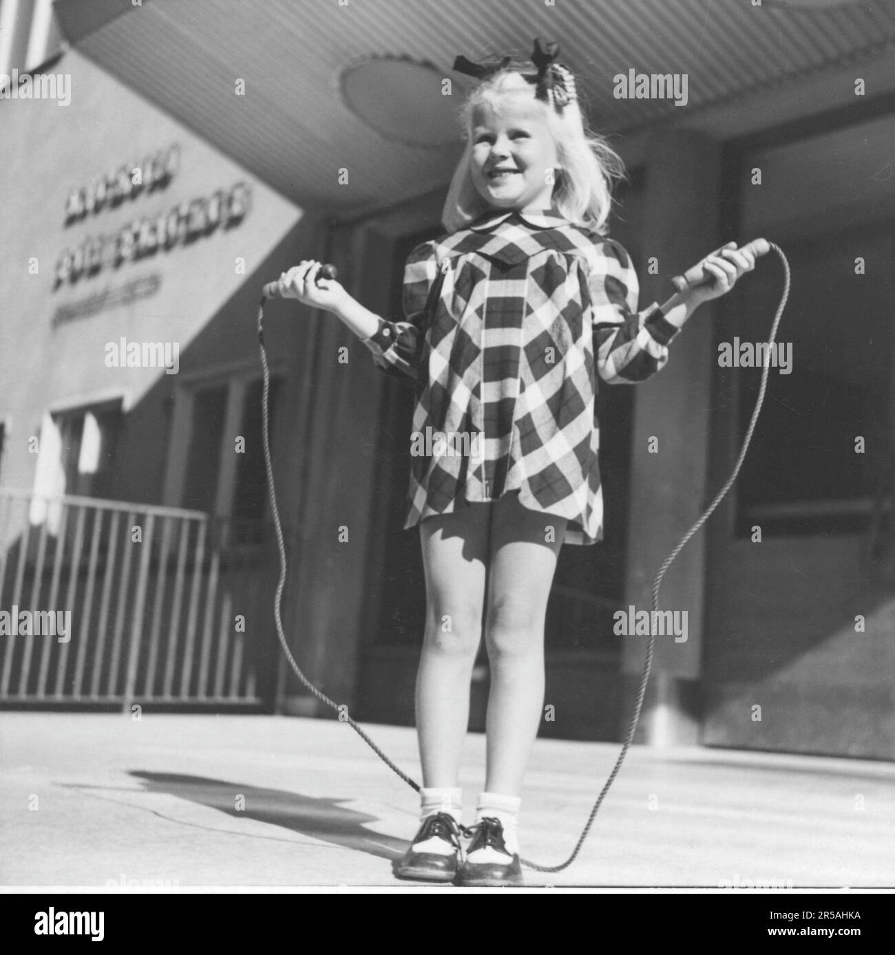 In the 1940s. A girl in a nice dress is jumping rope, skipping rope ...