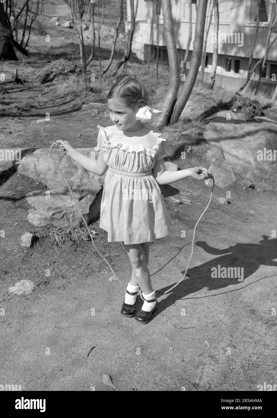 In the 1950s. A girl in a nice dress is jumping rope, skipping rope ...