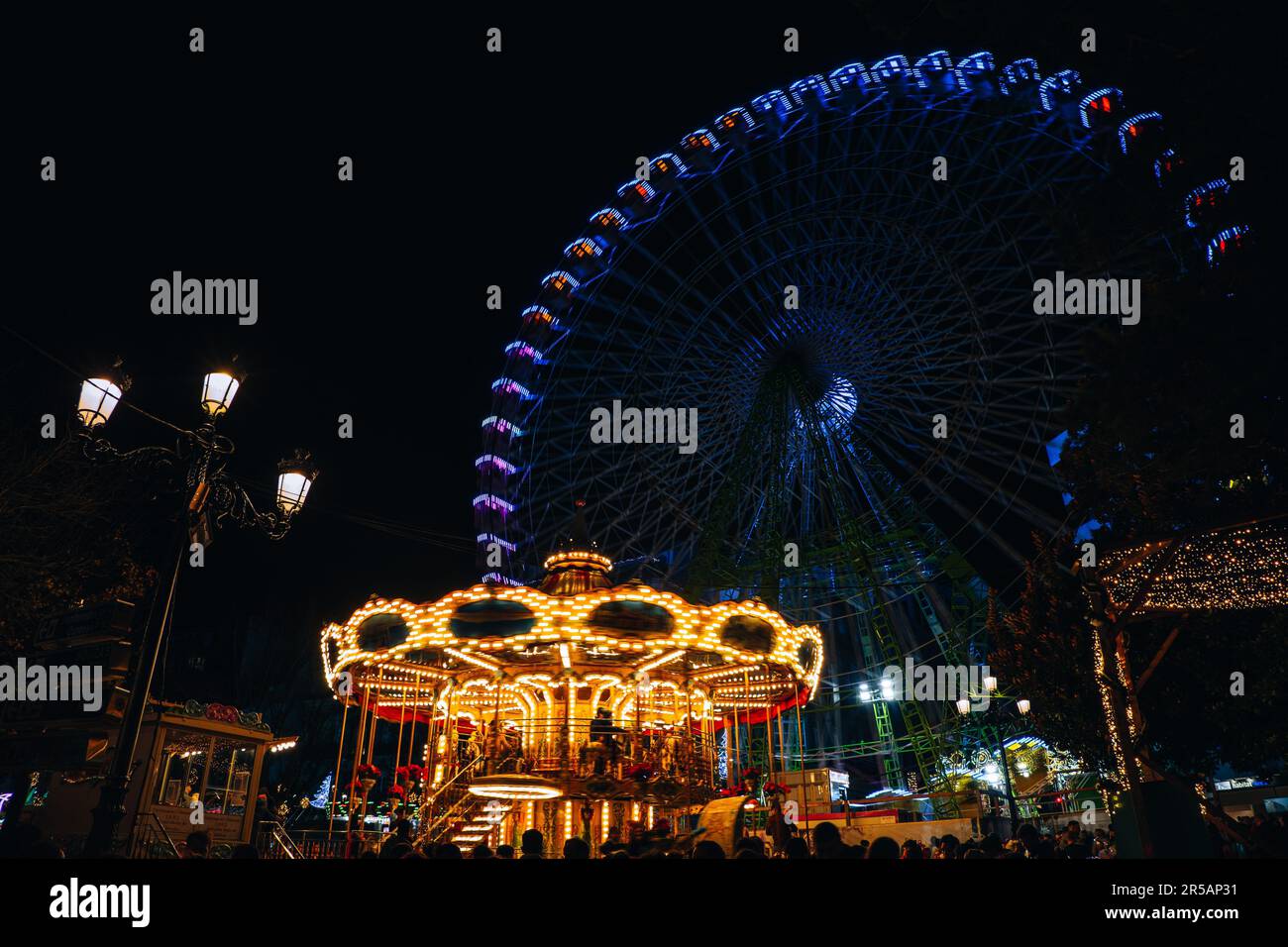A vibrant scene of a carnival-style amusement park, illuminated by ...