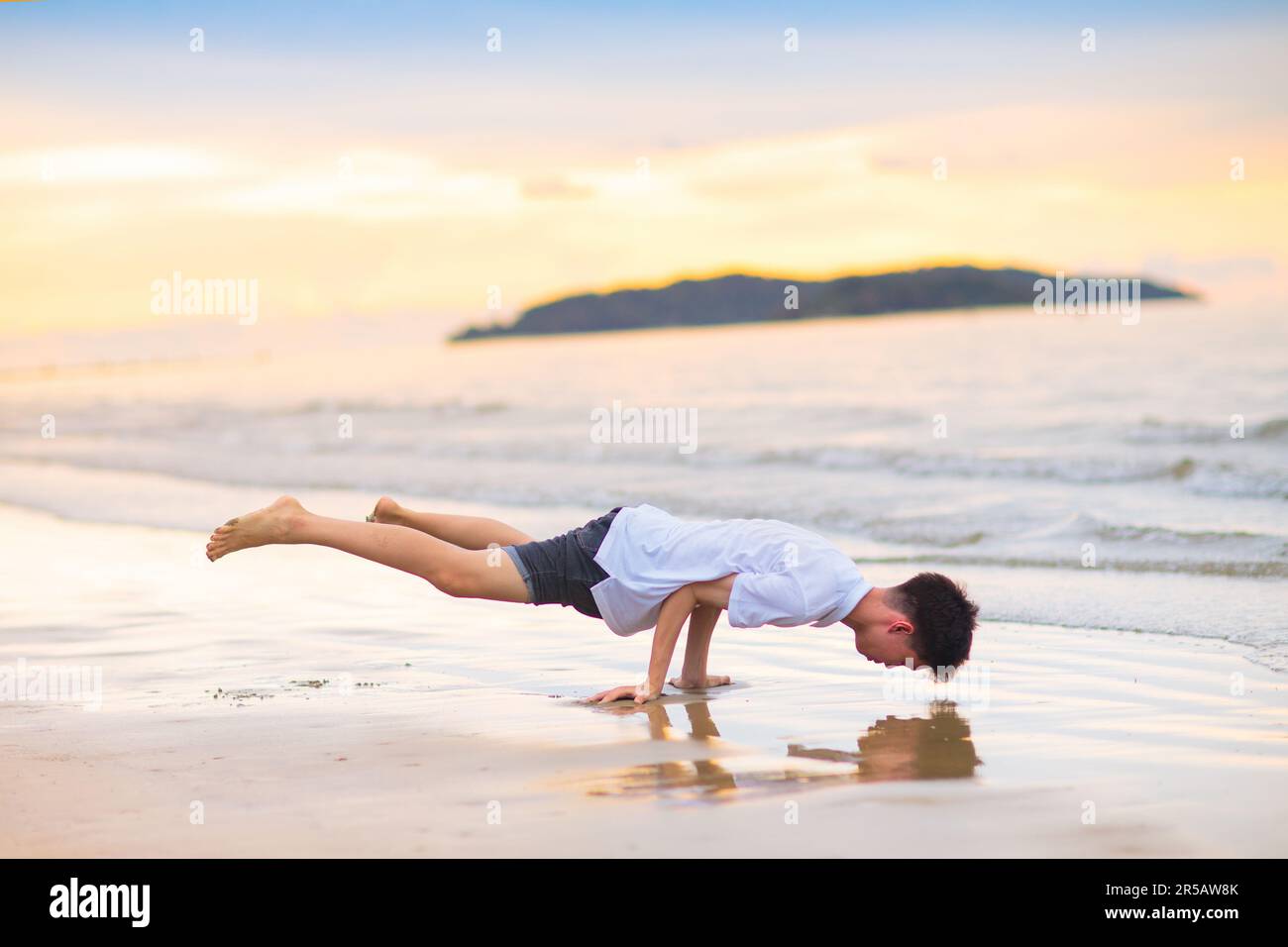 Teenager doing calisthenics exercise. Beach yoga at sunset. Teen boy ...