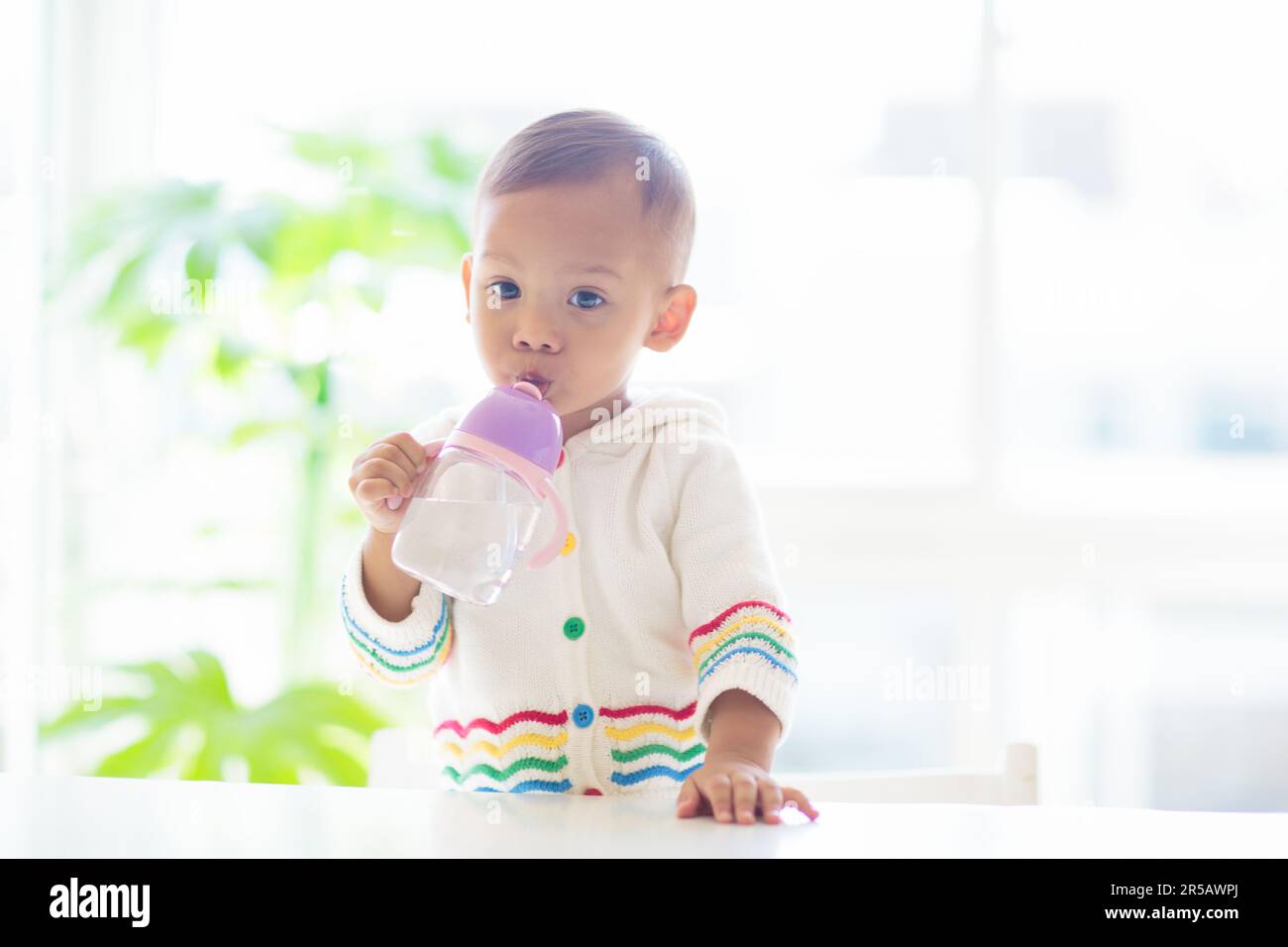 Baby eating and drinking in high chair. Asian baby boy with water ...