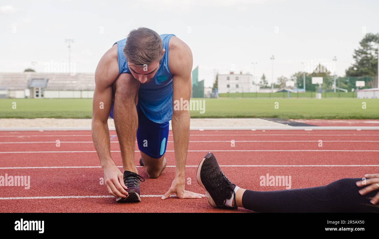 Young couple doing exercises on a running track, stretching legs and ...